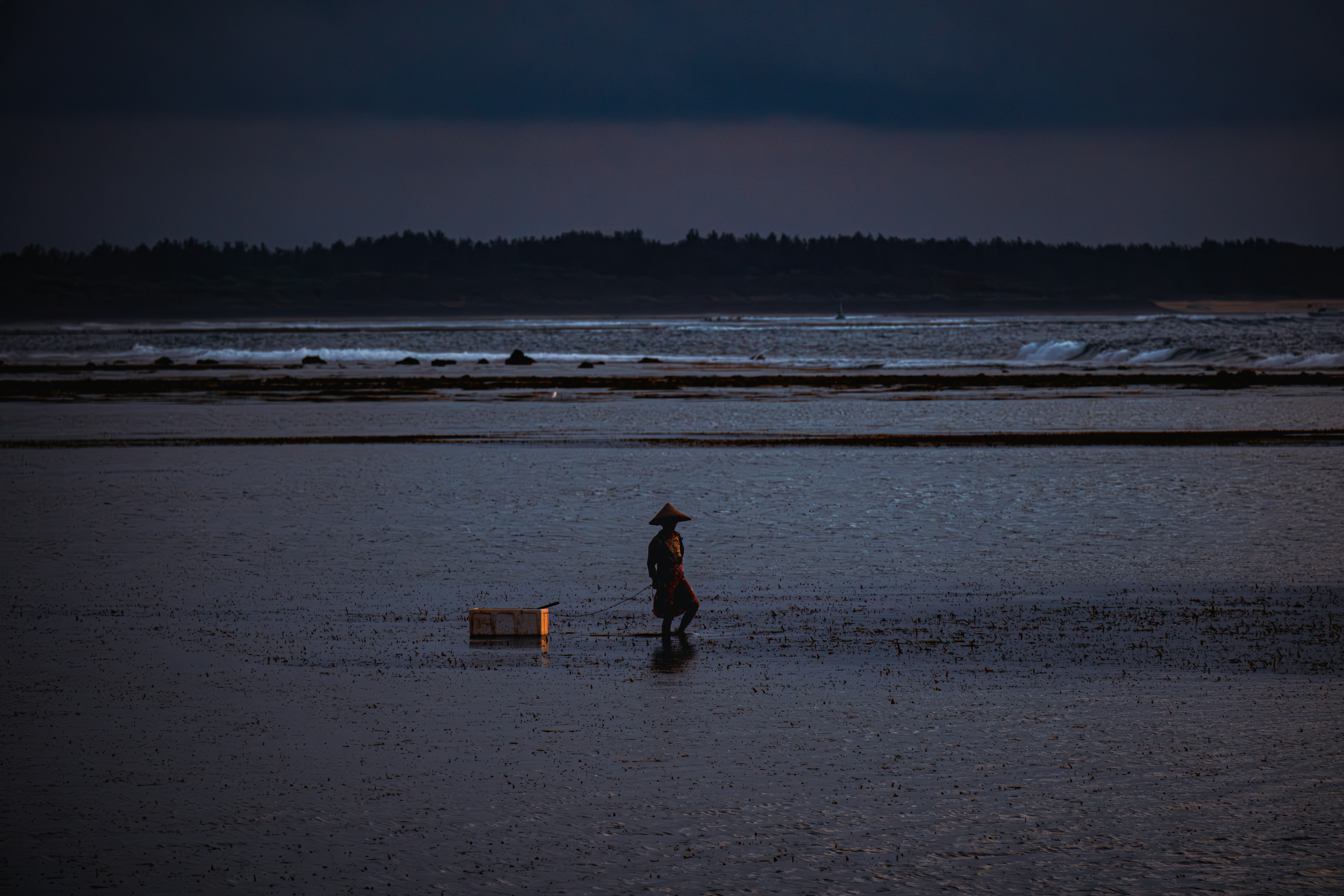 Dusk on the Tidal Plain: A lone figure and a crate in quiet blue light