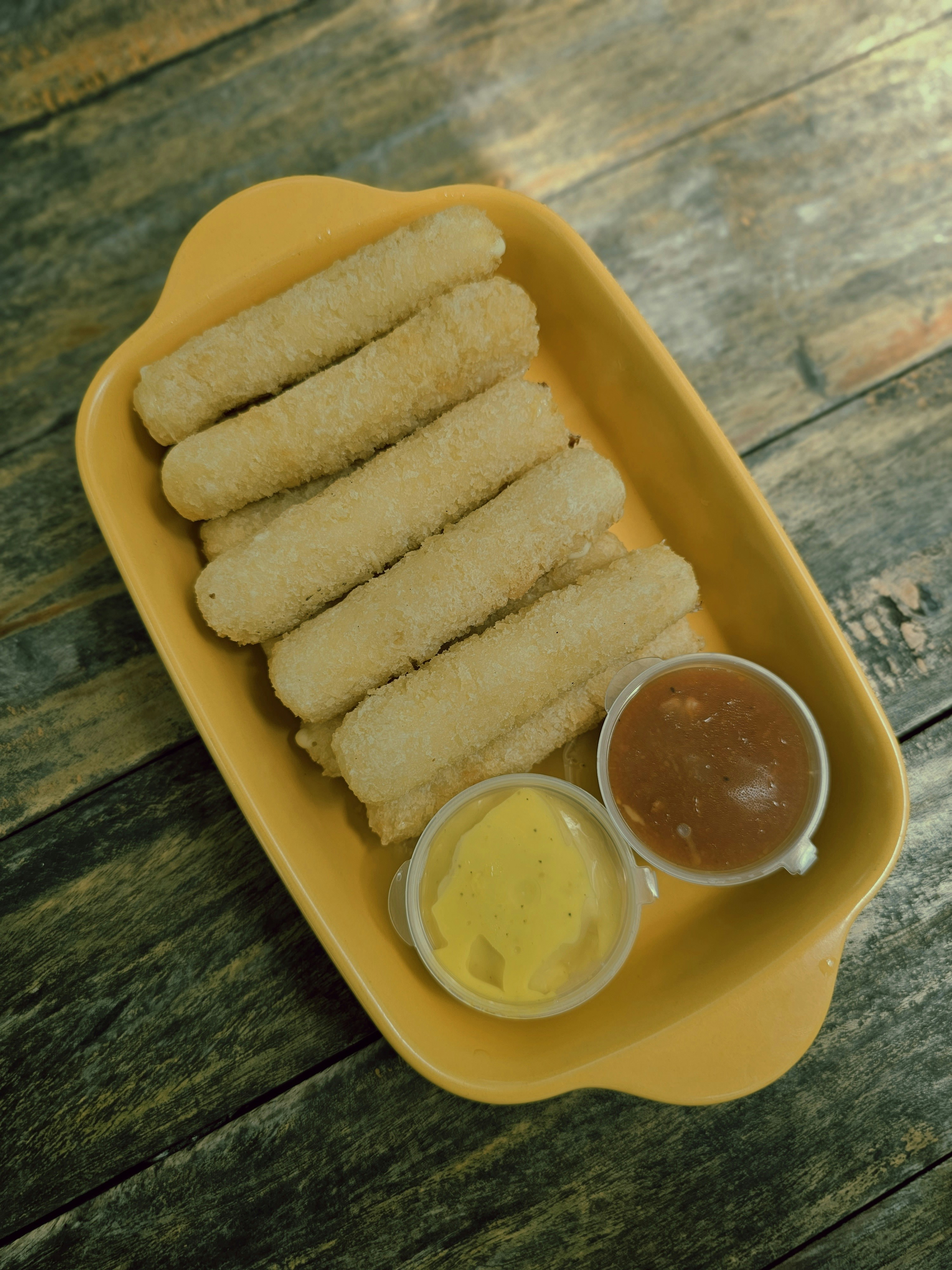 Plate of golden-brown cheese sticks accompanied by tangy dipping sauces on a rustic wooden table.