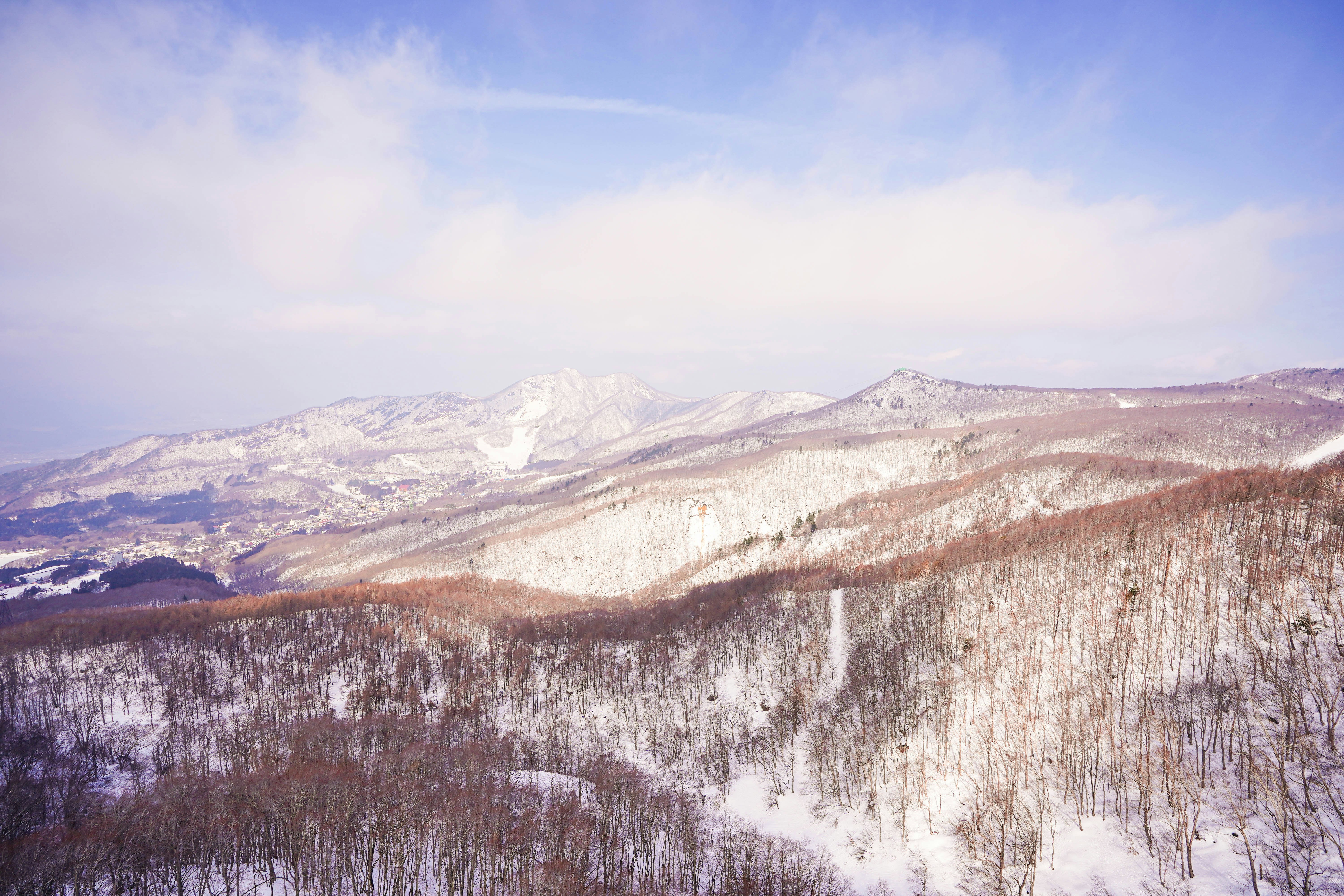 Snow-covered mountain range under a bright blue sky with scattered clouds.