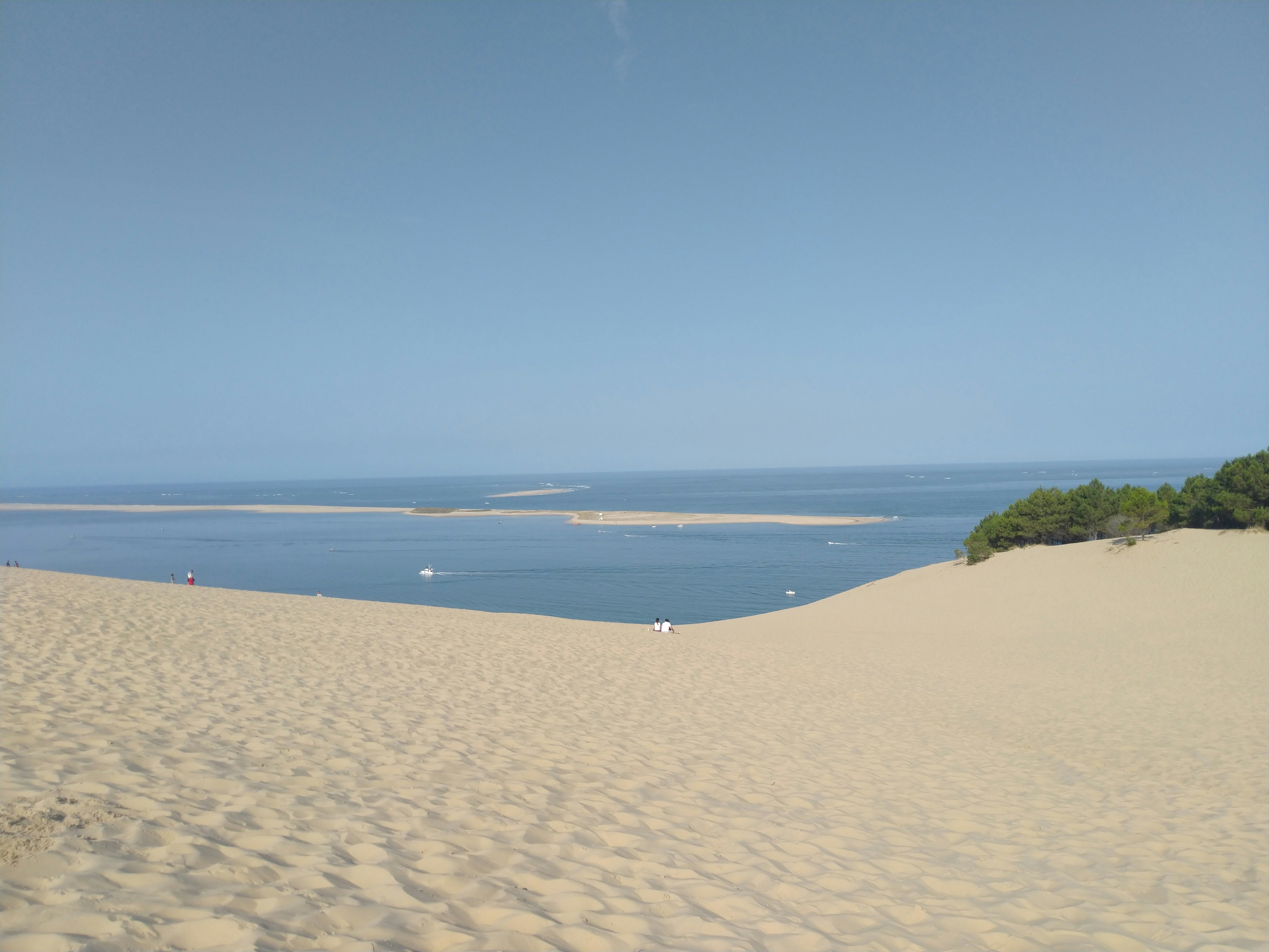 Vast sandy dune meeting a calm blue ocean under a clear sky.