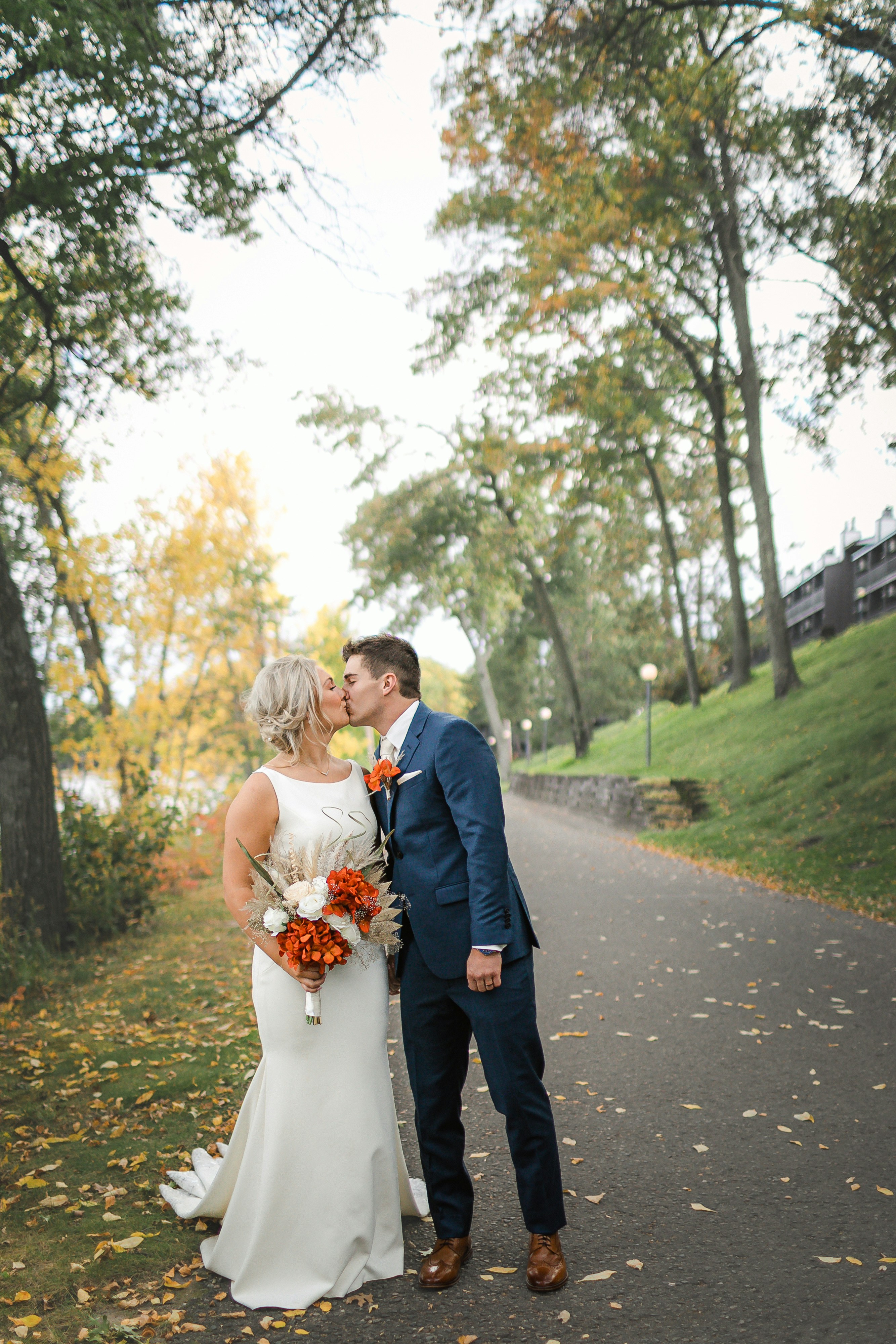 A bride and groom kissing on a path surrounded by trees photo – Free ...