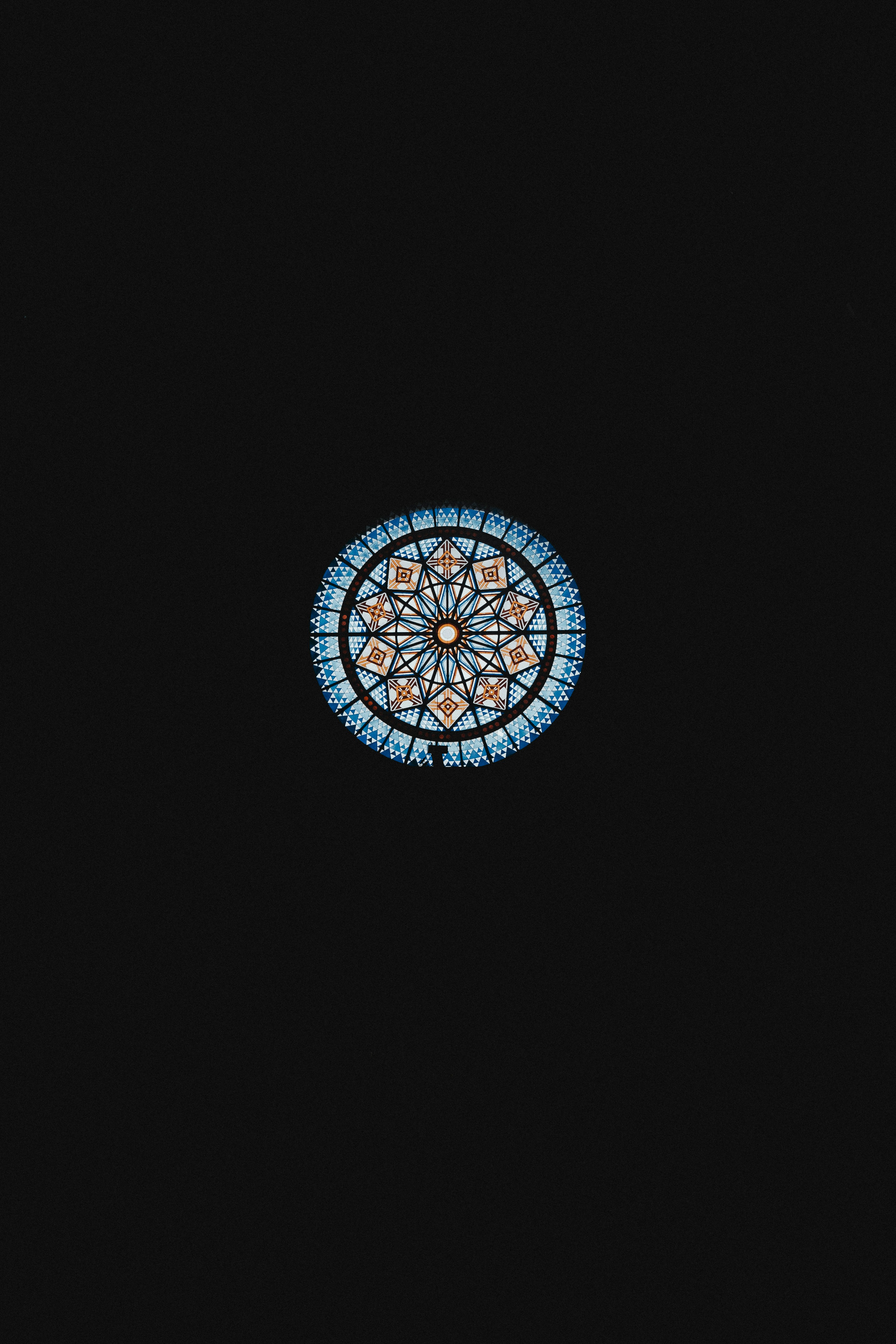 Circular stained-glass rose window glowing with blue and copper tones against a dark night sky.