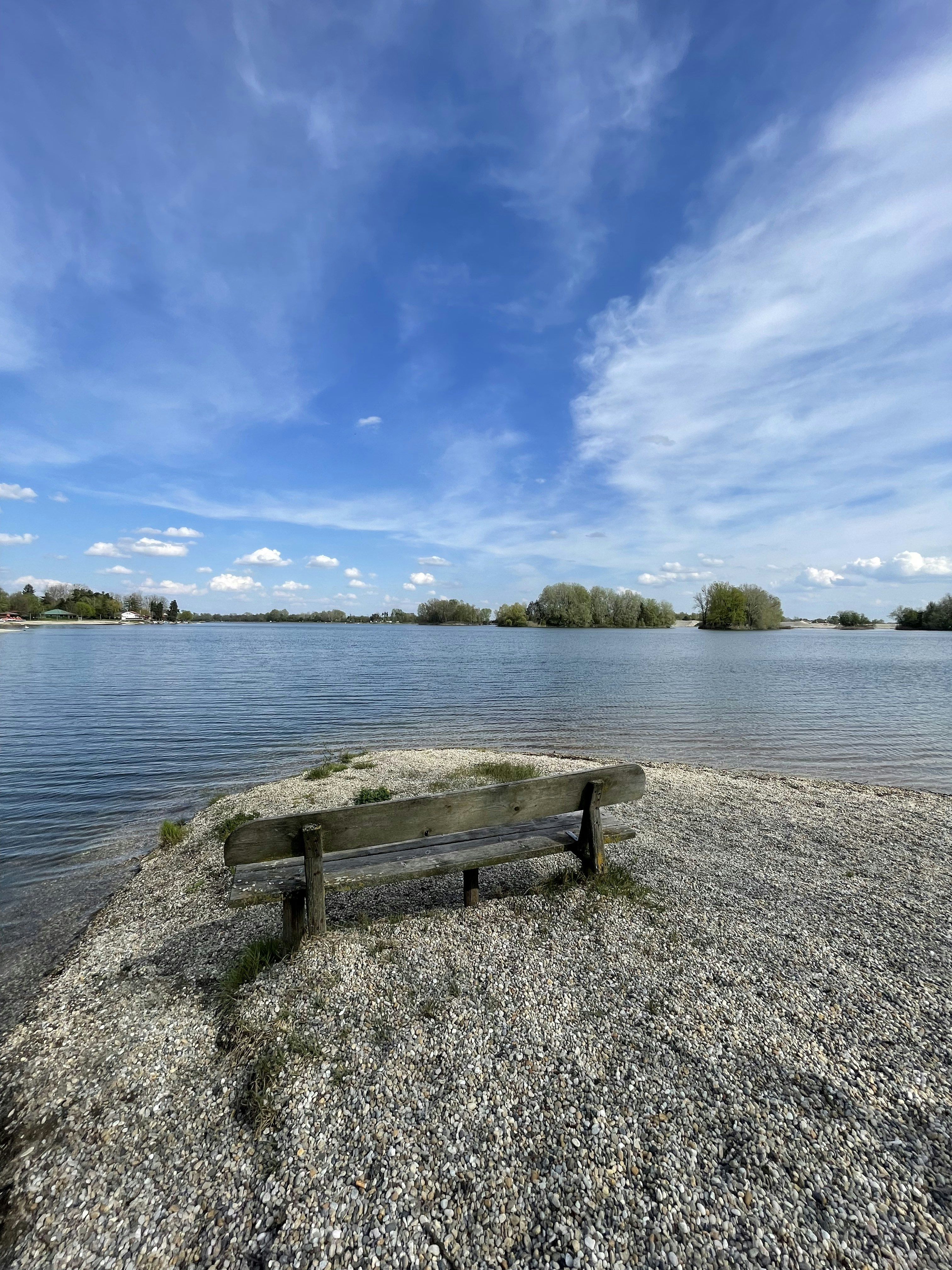 A Quiet Riverside Bench Anchored by Pebbles Beneath a Vast Sky