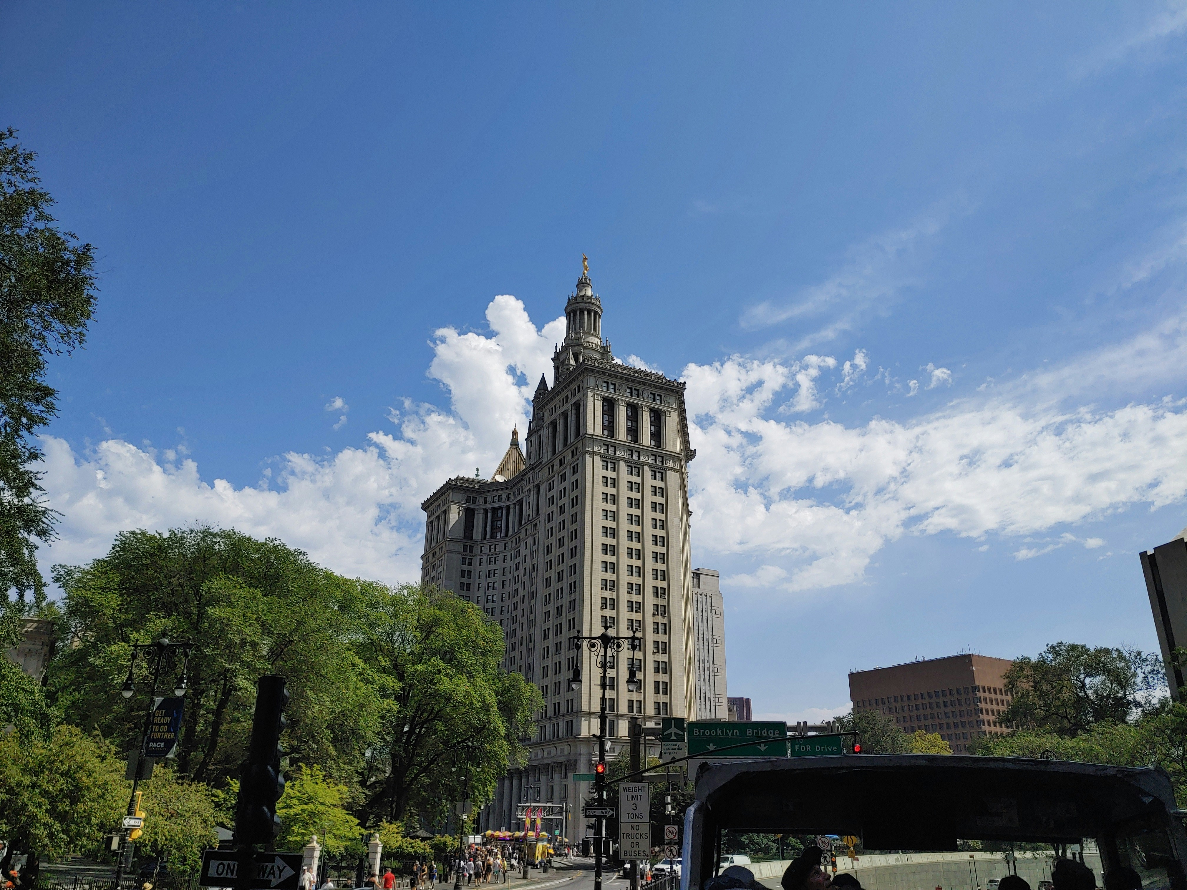 Tall building with ornate architecture framed by lush trees and a vibrant blue sky.