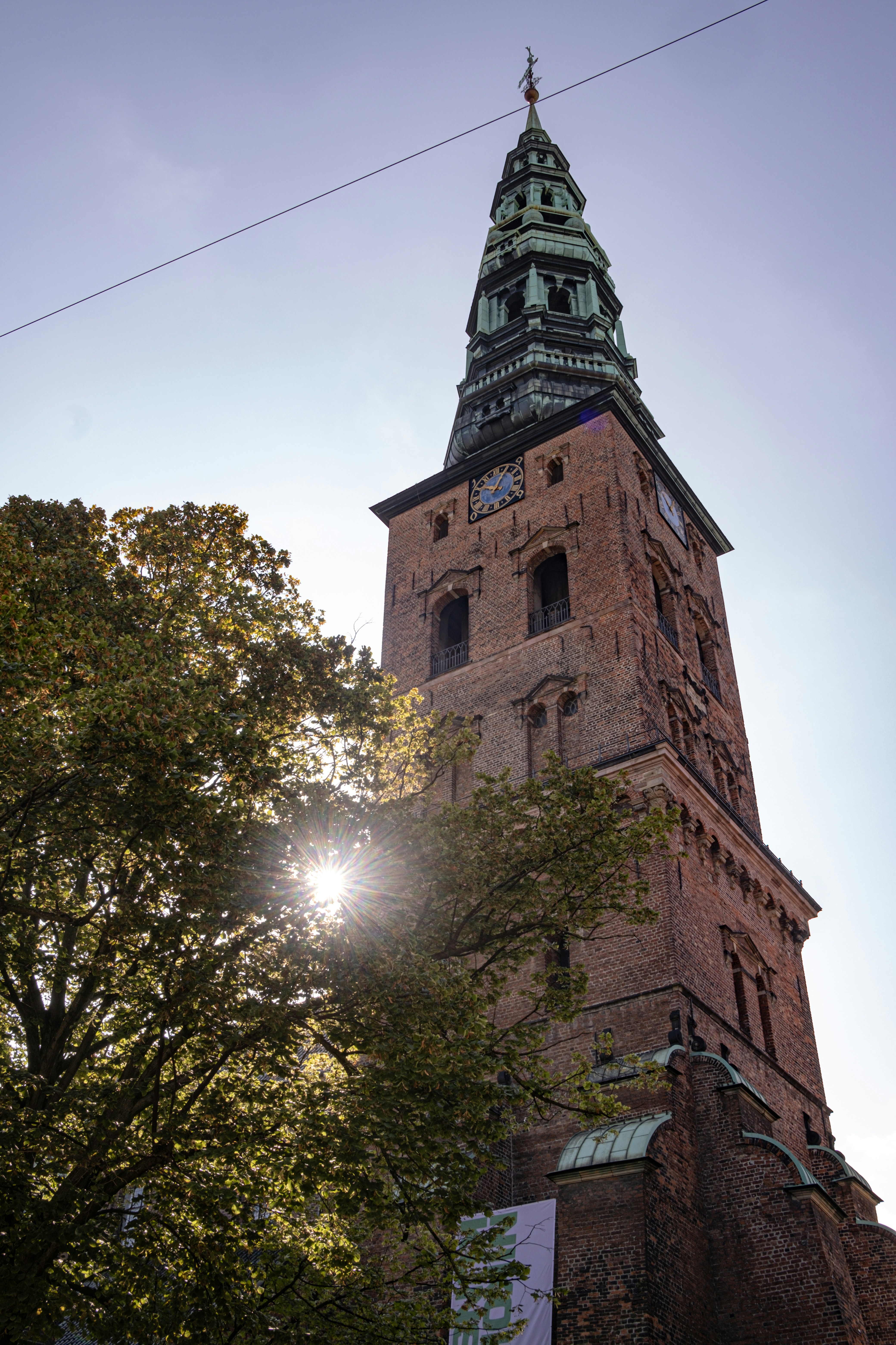 Sunlit Spire Through a Leafy Frame: A Brick Clocktower in Backlight
