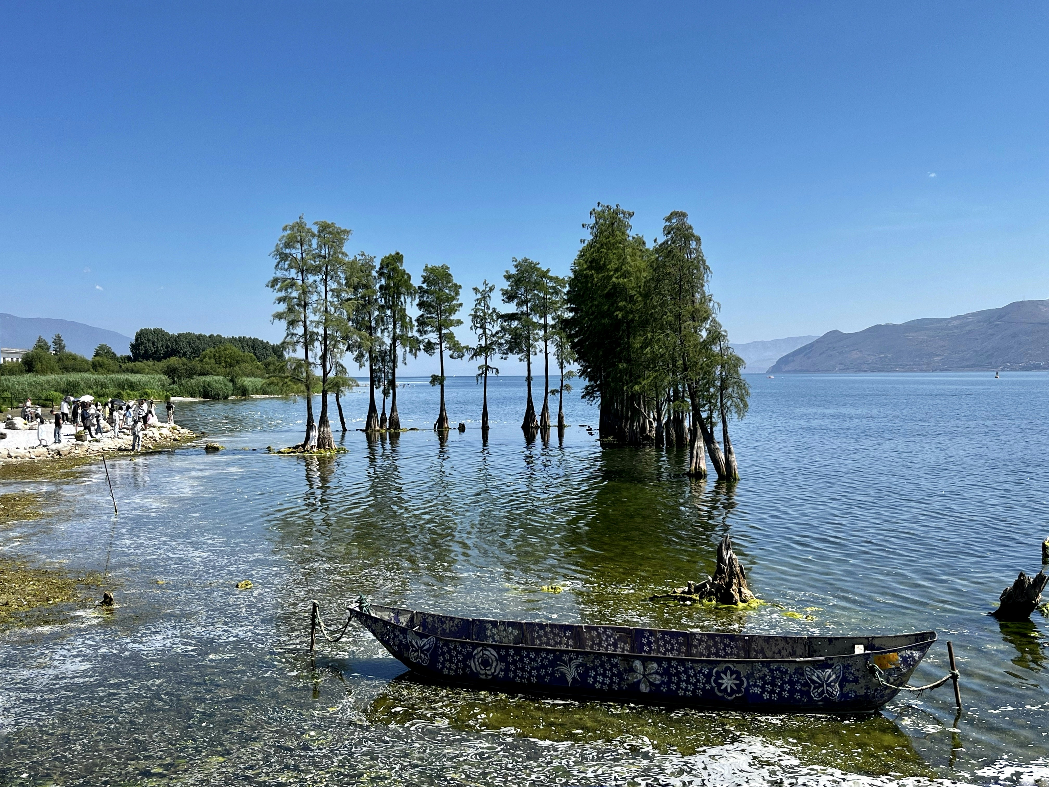 Traditional boat anchored in a tranquil lake surrounded by lush trees and distant mountains. The scene captures the harmony of water and land.