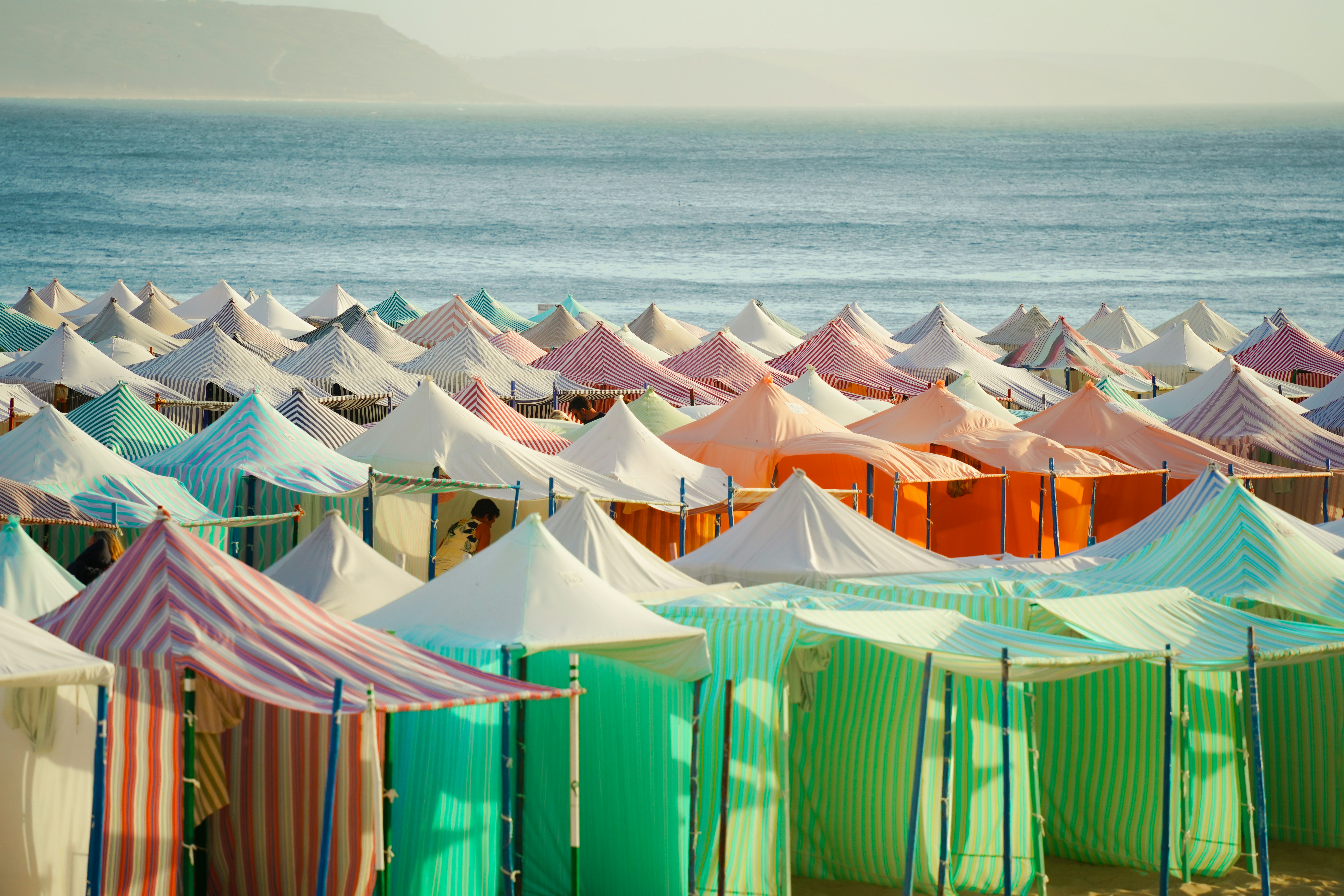 Vibrant beach tents in a variety of colors create a patchwork effect against the backdrop of the ocean. The scene captures the essence of a lively seaside atmosphere.