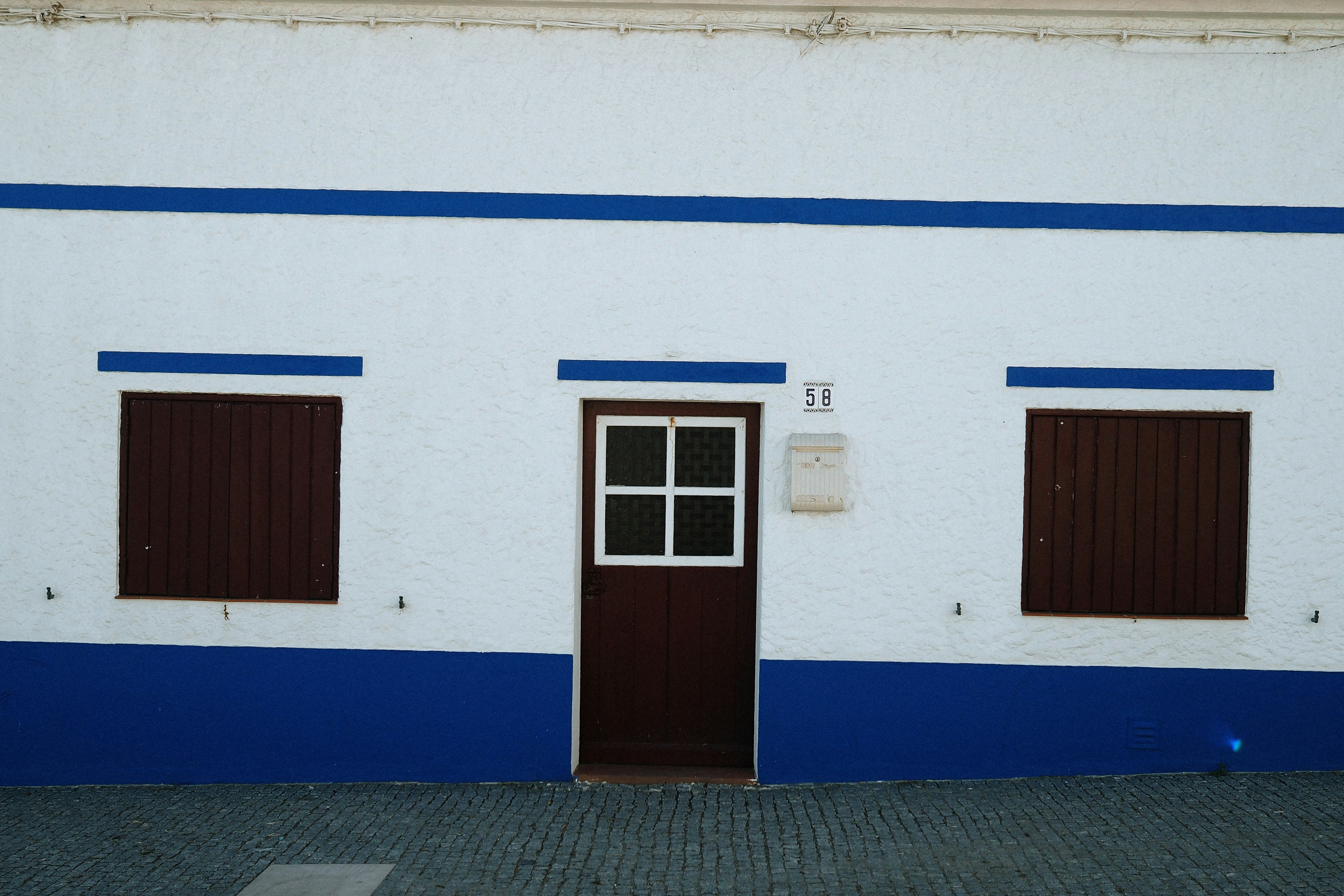 White facade with blue accents and closed brown shutters framing a central door.