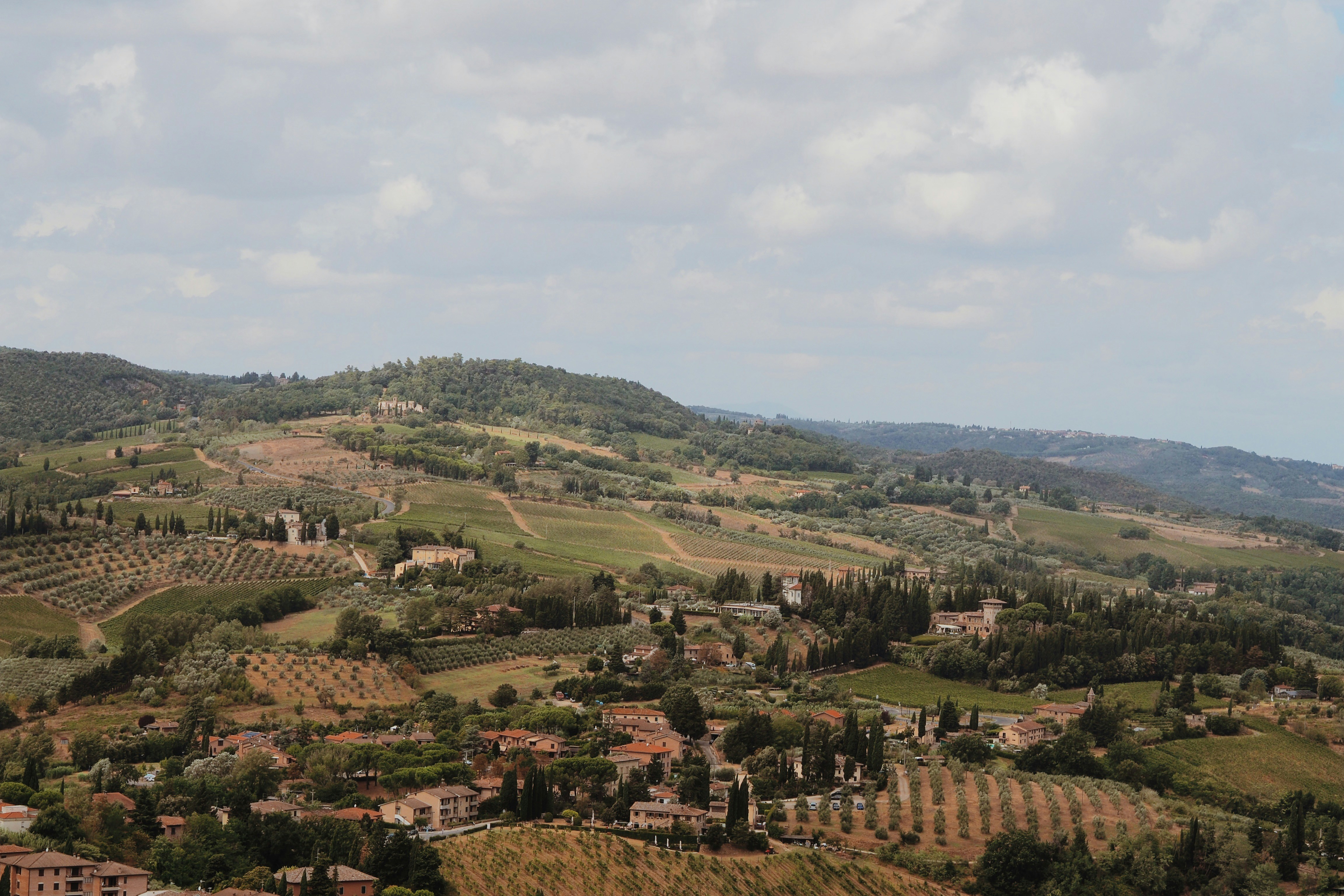 Expansive view of Tuscany's rolling hills dotted with rustic buildings and lush vineyards under a cloudy sky.