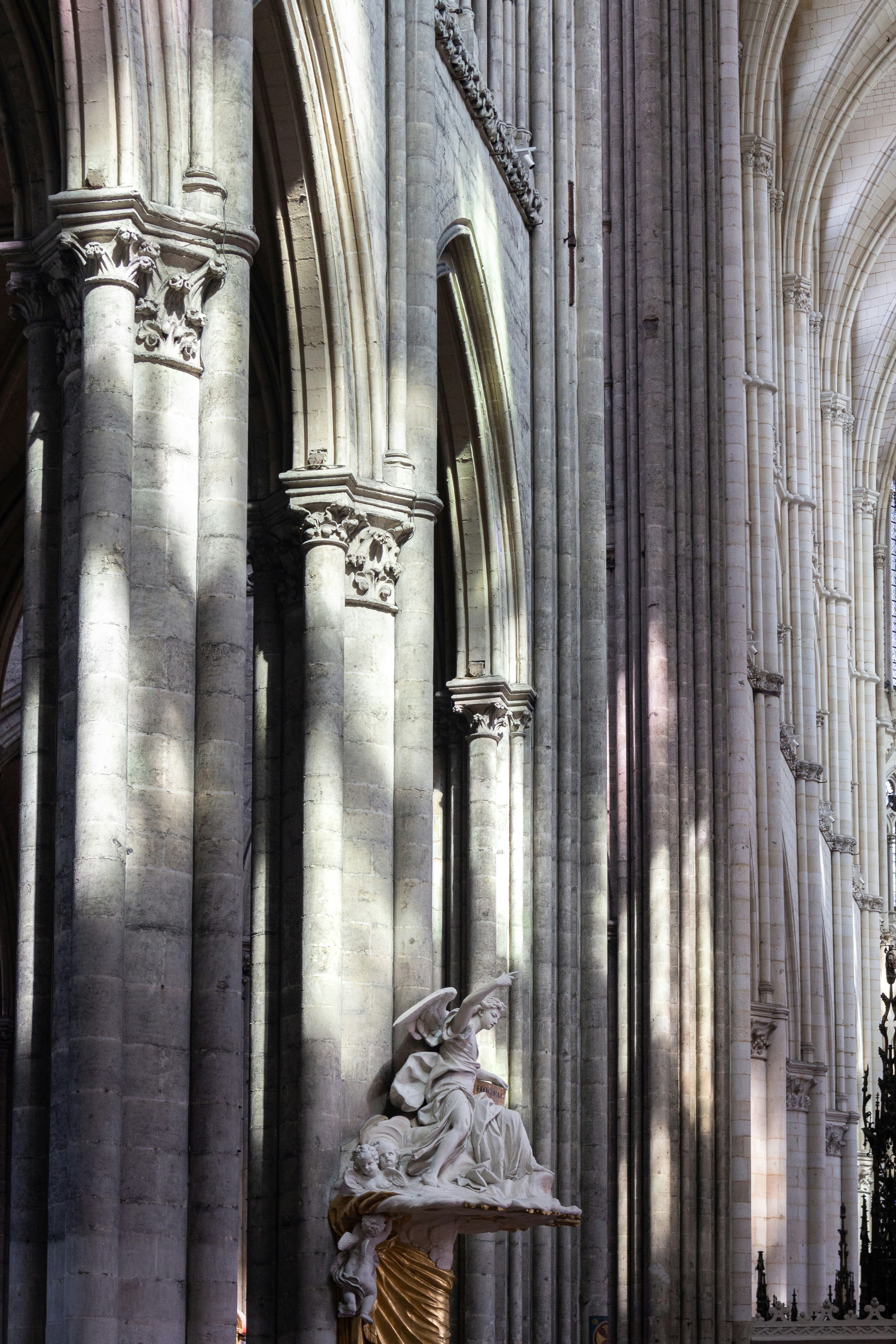 Marble Angel Amid Gothic Columns: Light Weaving Through the Cathedral Facade