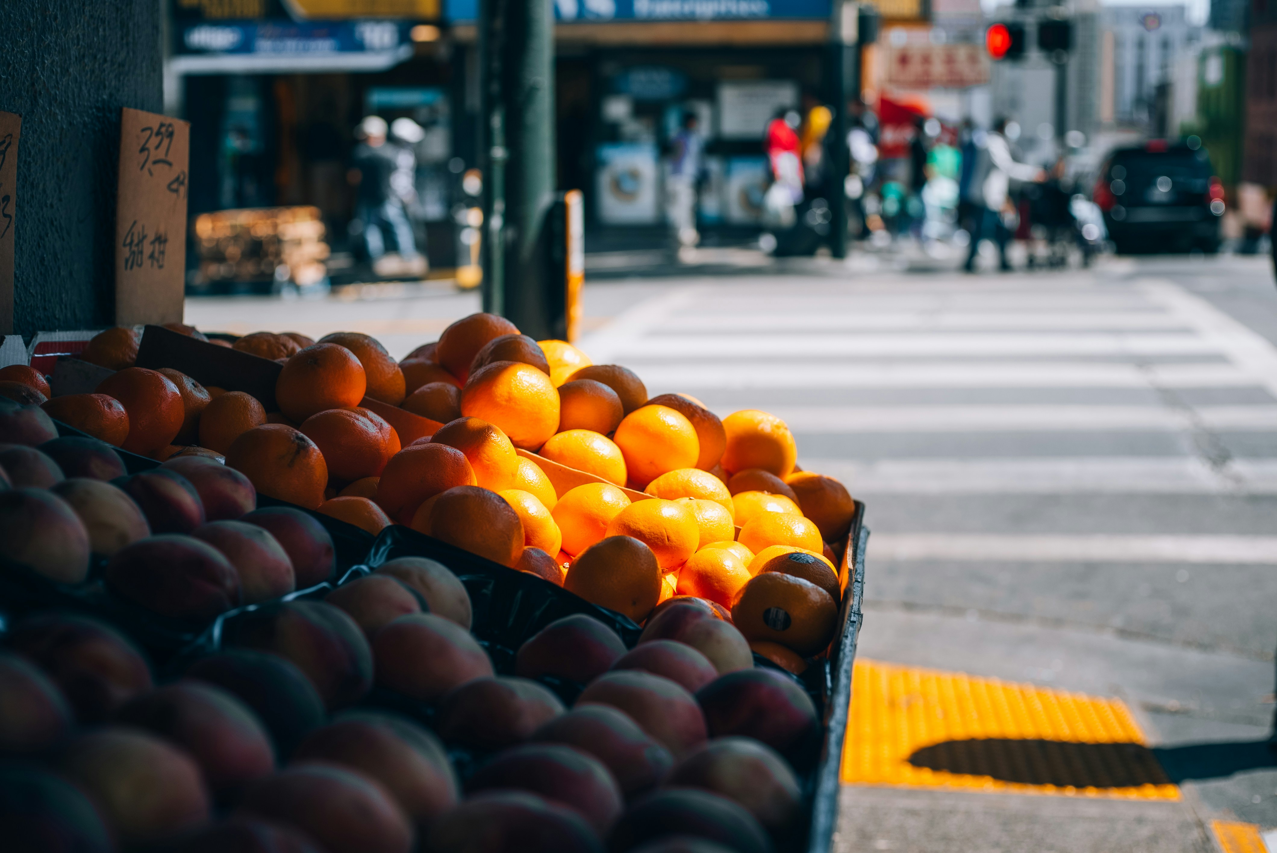 Sunlit Citrus at a City Market: Oranges in Focus Amid Urban Flow