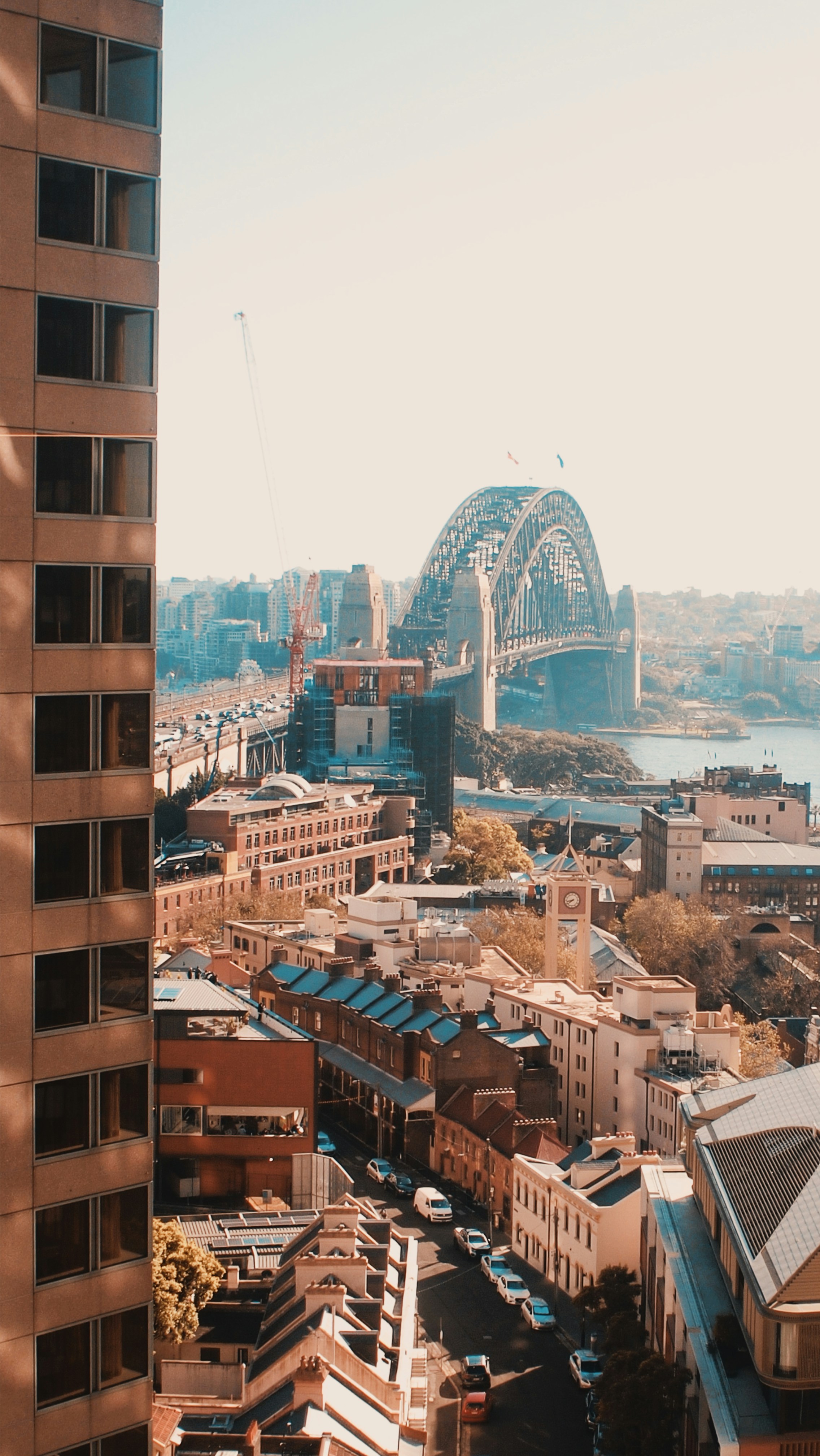 Aerial cityscape showing a large arch bridge crossing a river, with dense mid-rise streets bathed in warm light.