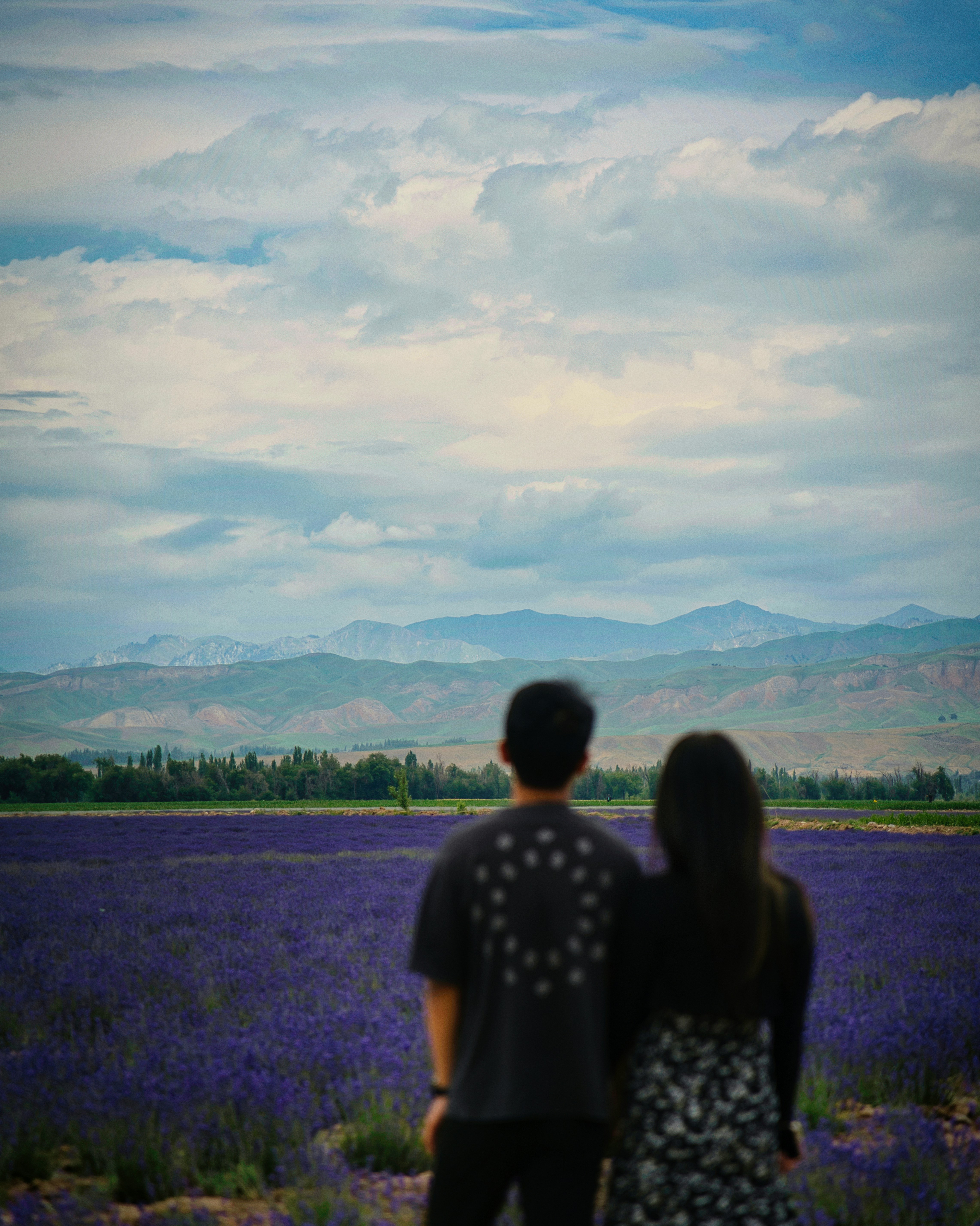 Two Silhouettes Over a Lavender Sea Beneath Layered Mountain Skies