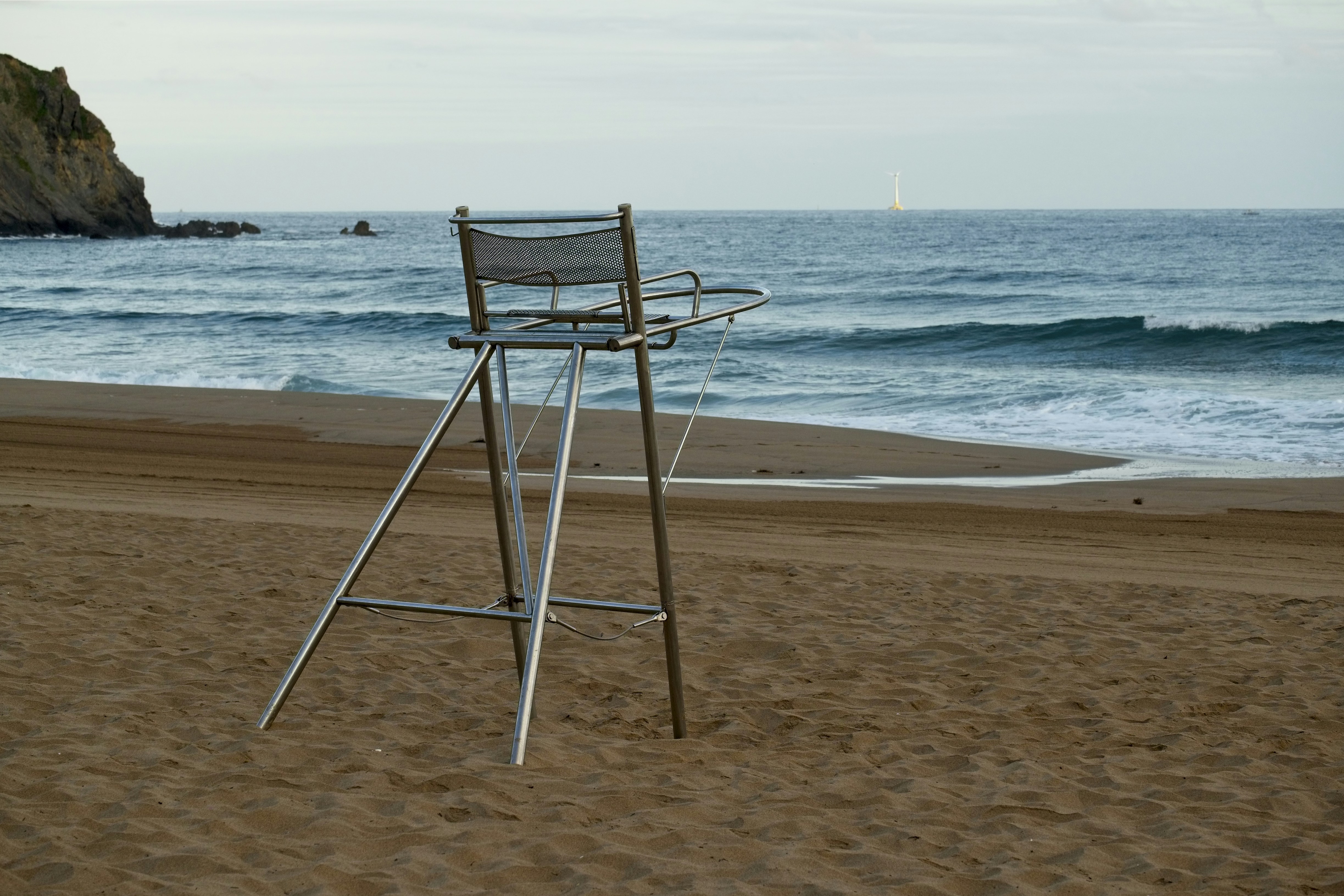 The Watcher on the Sand: Lifeguard Chair Framed by Sea and Distant Sail