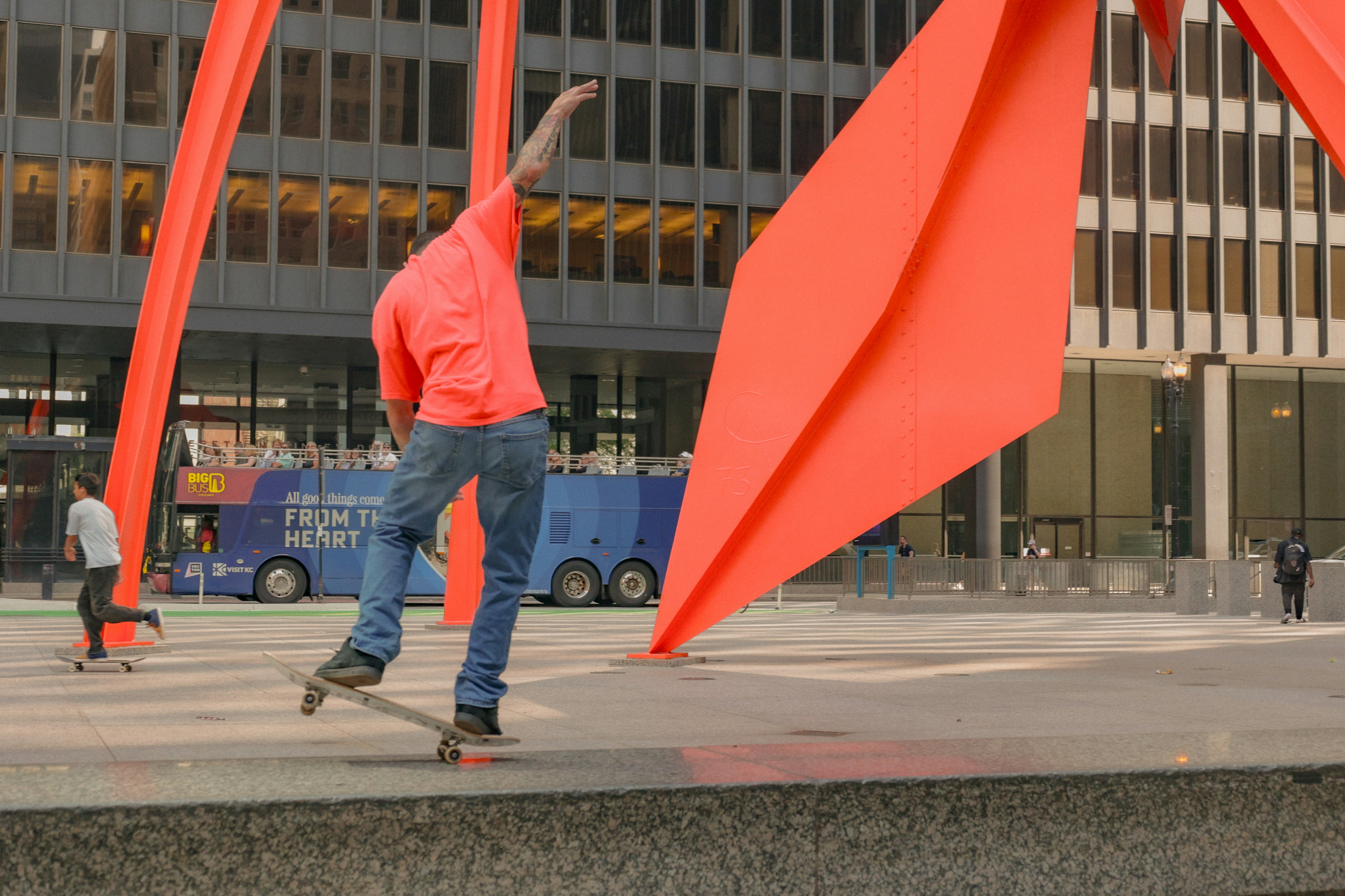 Skateboarder in Neon Coral Gliding by a Monumental Red Angular Sculpture