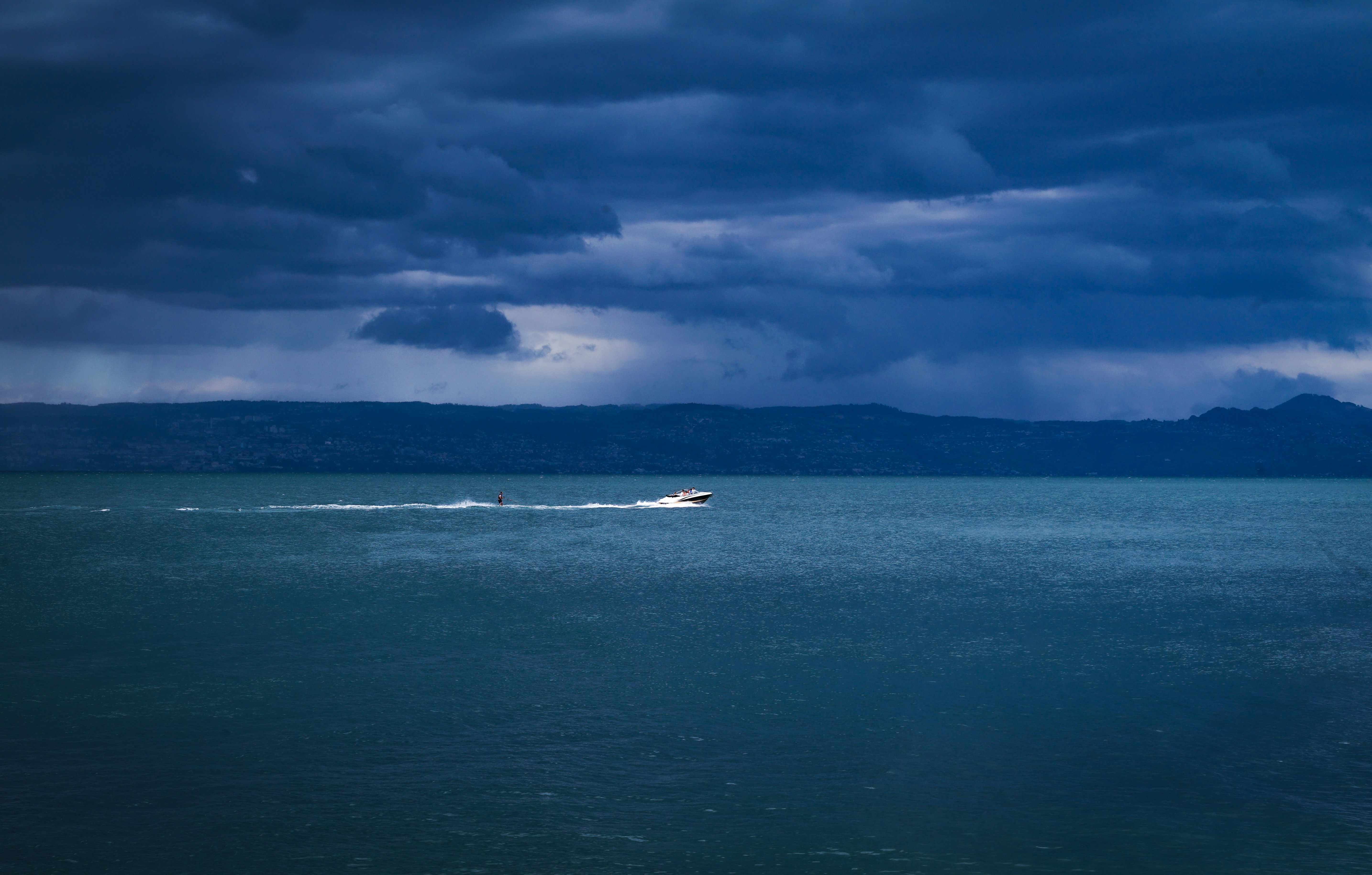 Lone Speedboat Tracing a Silvery Wake Across a Stormy Blue Horizon