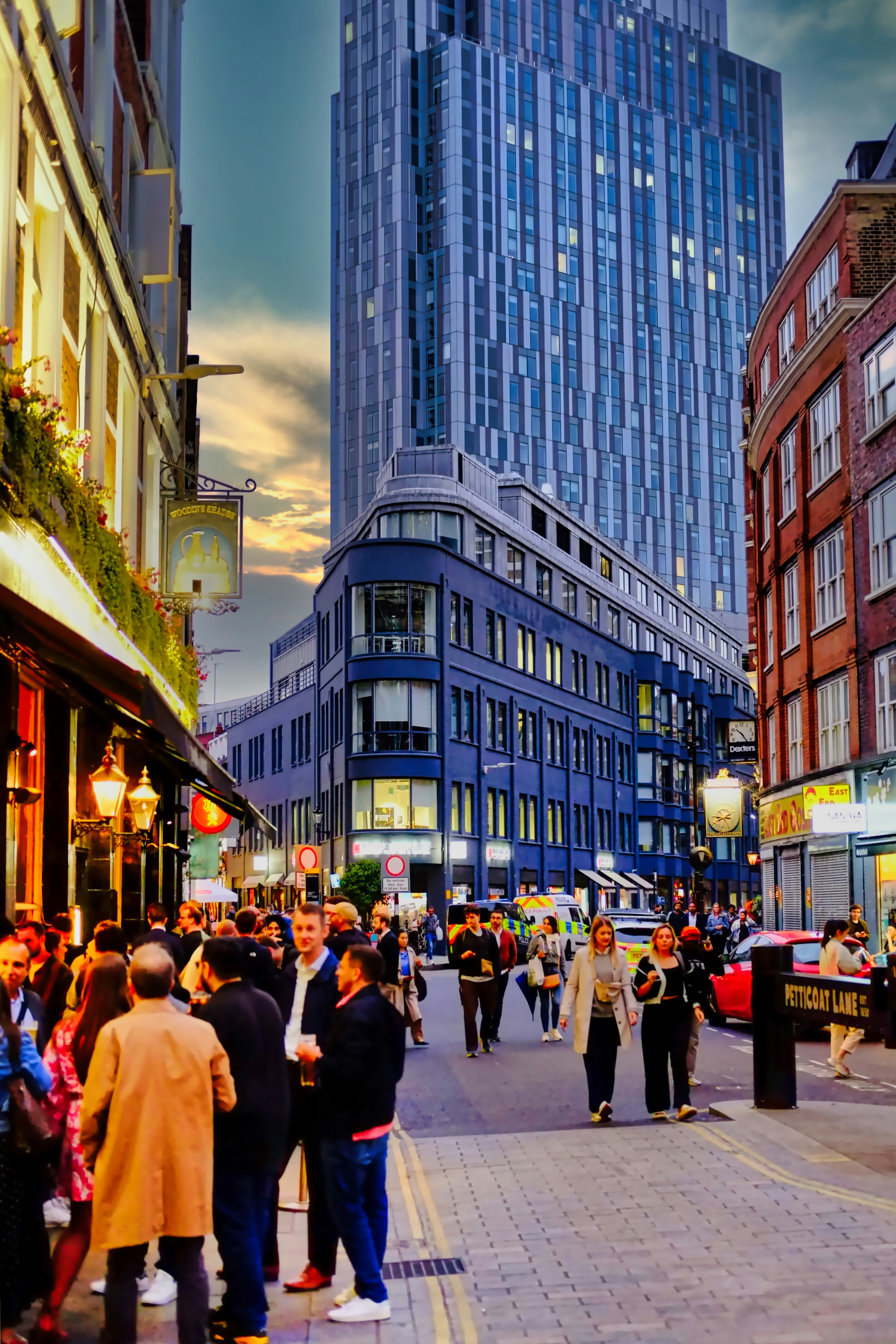 Bustling street scene at dusk with pedestrians mingling and modern architecture towering in the background.