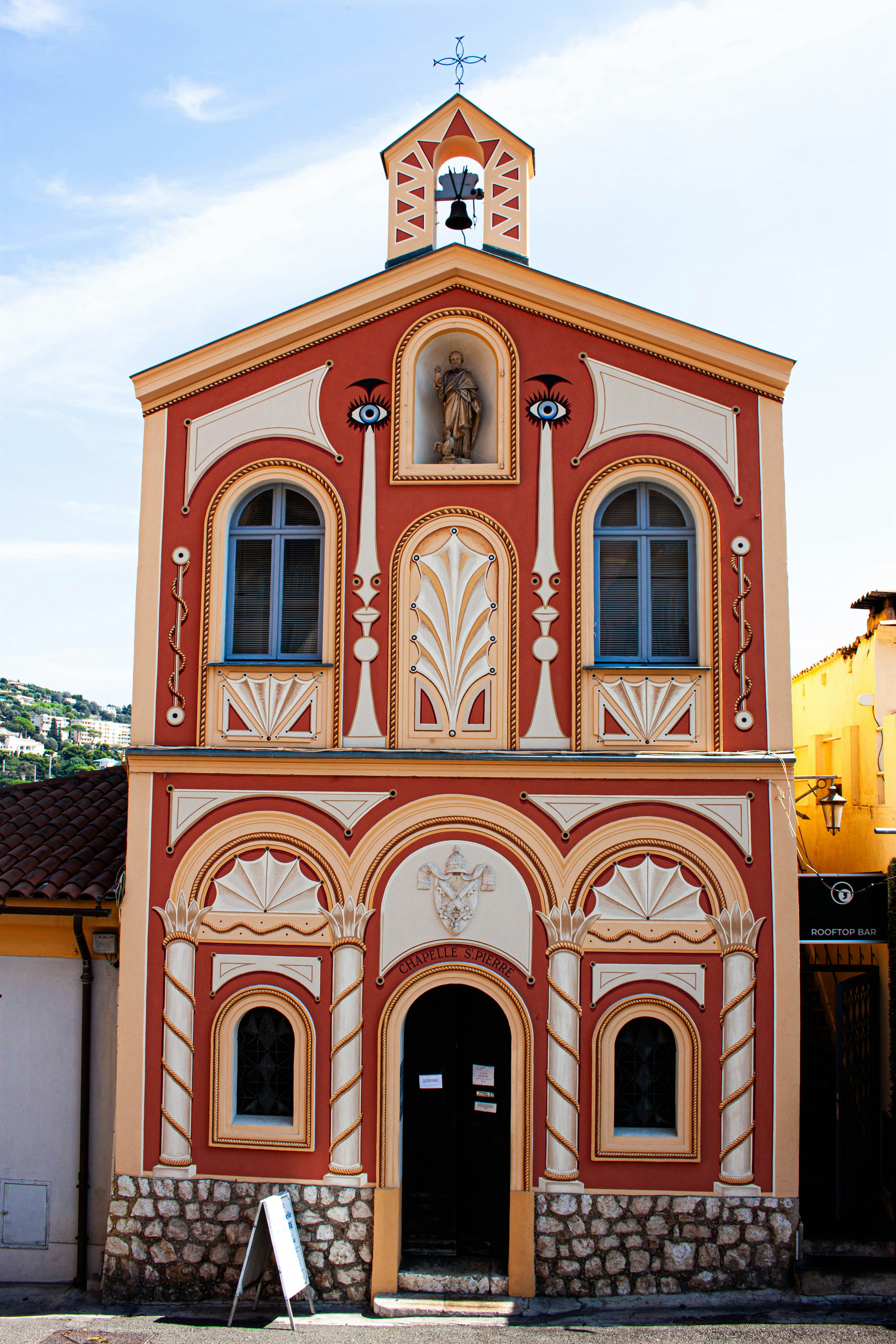 Coral Facade at Noon: A Mediterranean Chapel Revealing a Central Niche and Ornate Arches