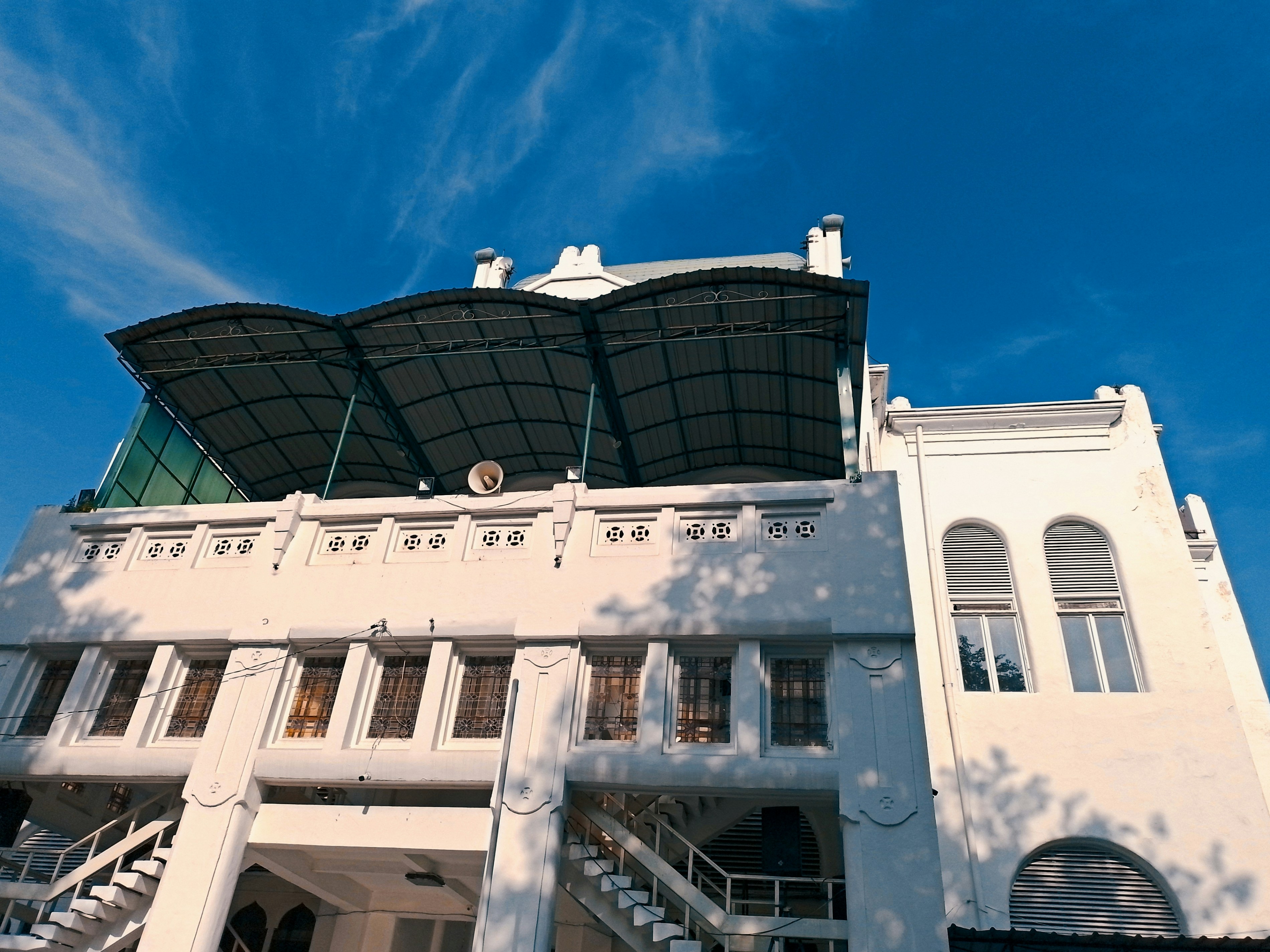 Colonial-style mosque with prominent arches and staircases under a vibrant blue sky.