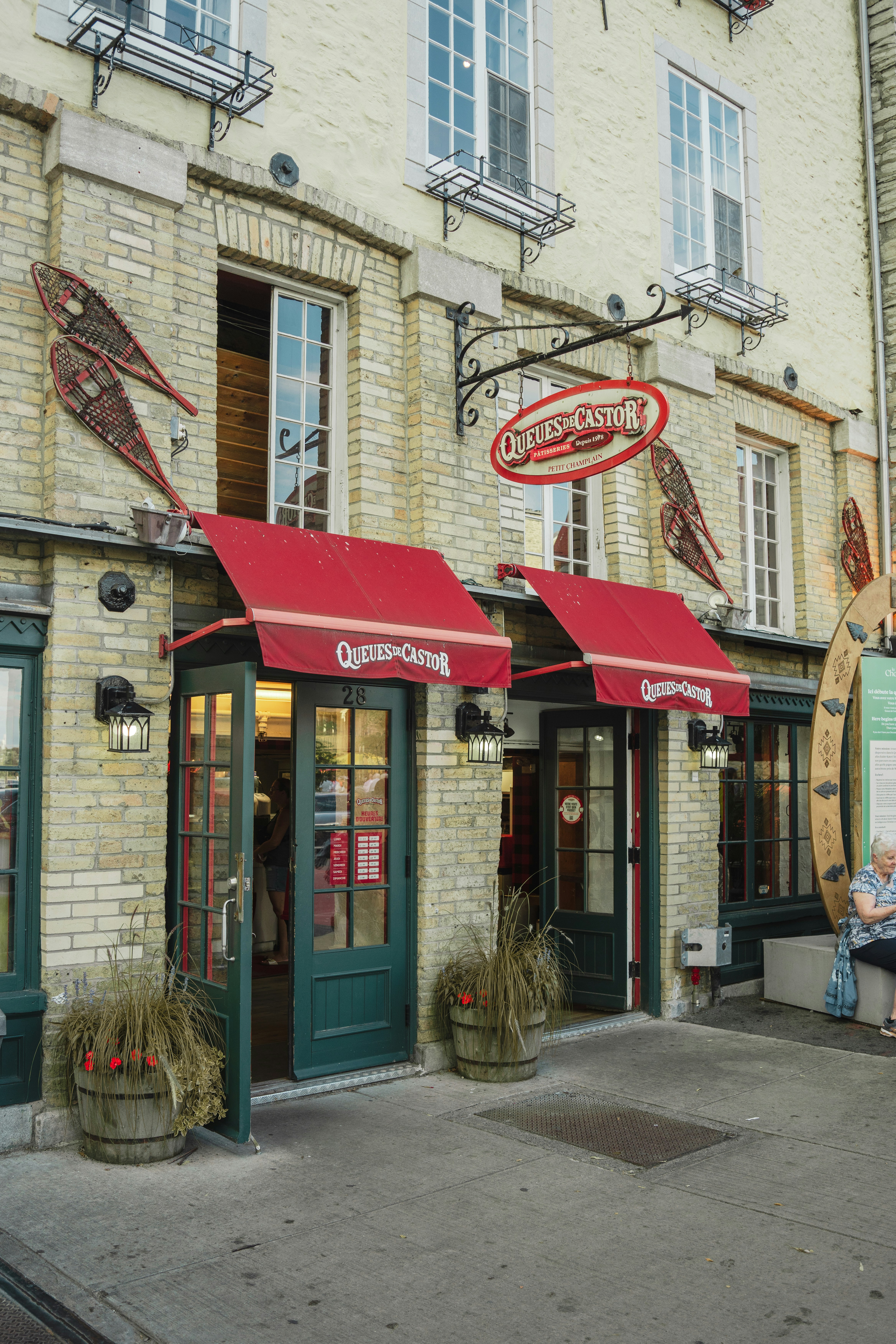 a brick building with red awnings and a woman sitting on a bench