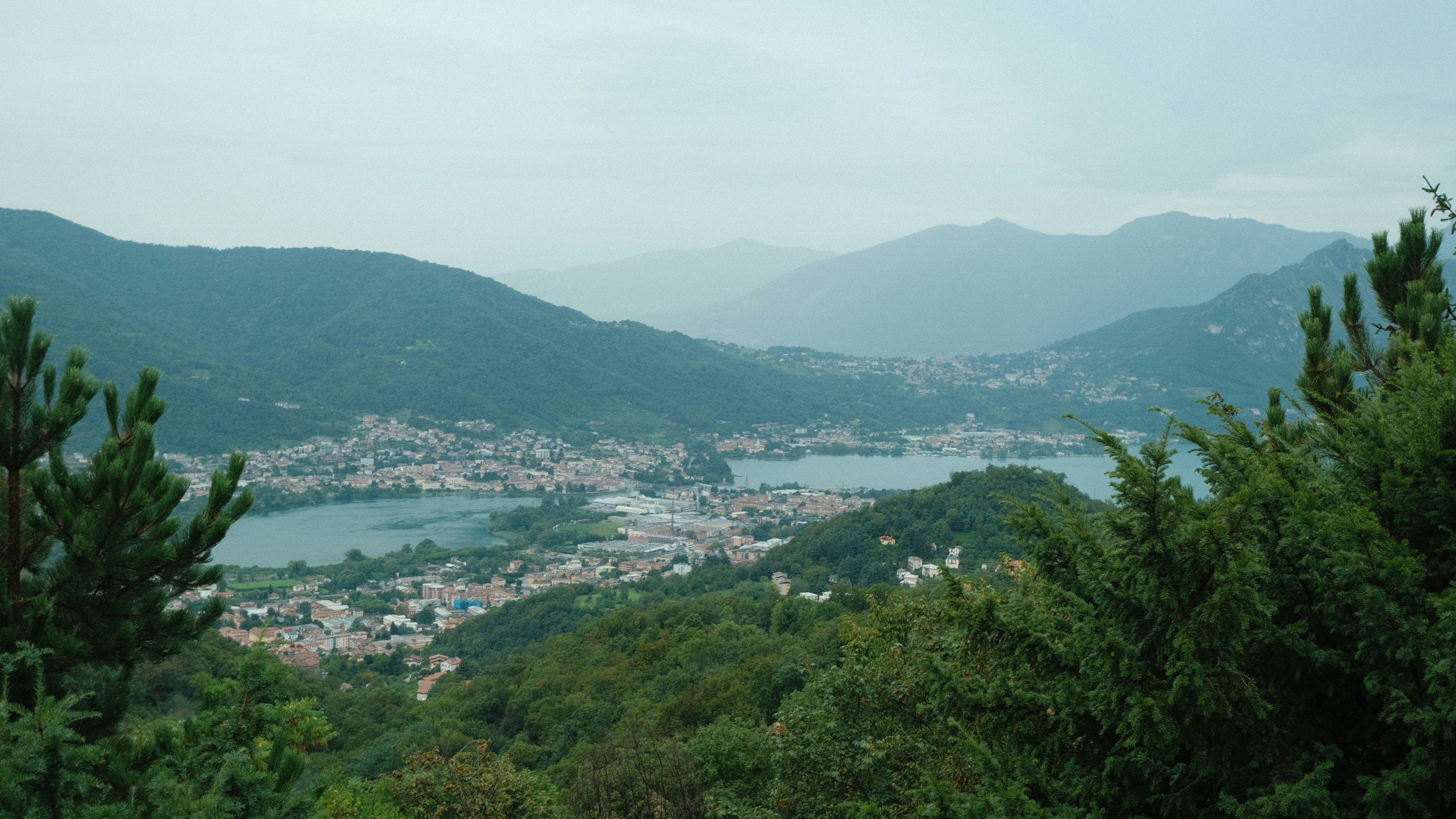 A panoramic view of Lago Maggiore framed by lush hills and distant mountains, showcasing a tranquil town nestled by the water's edge.