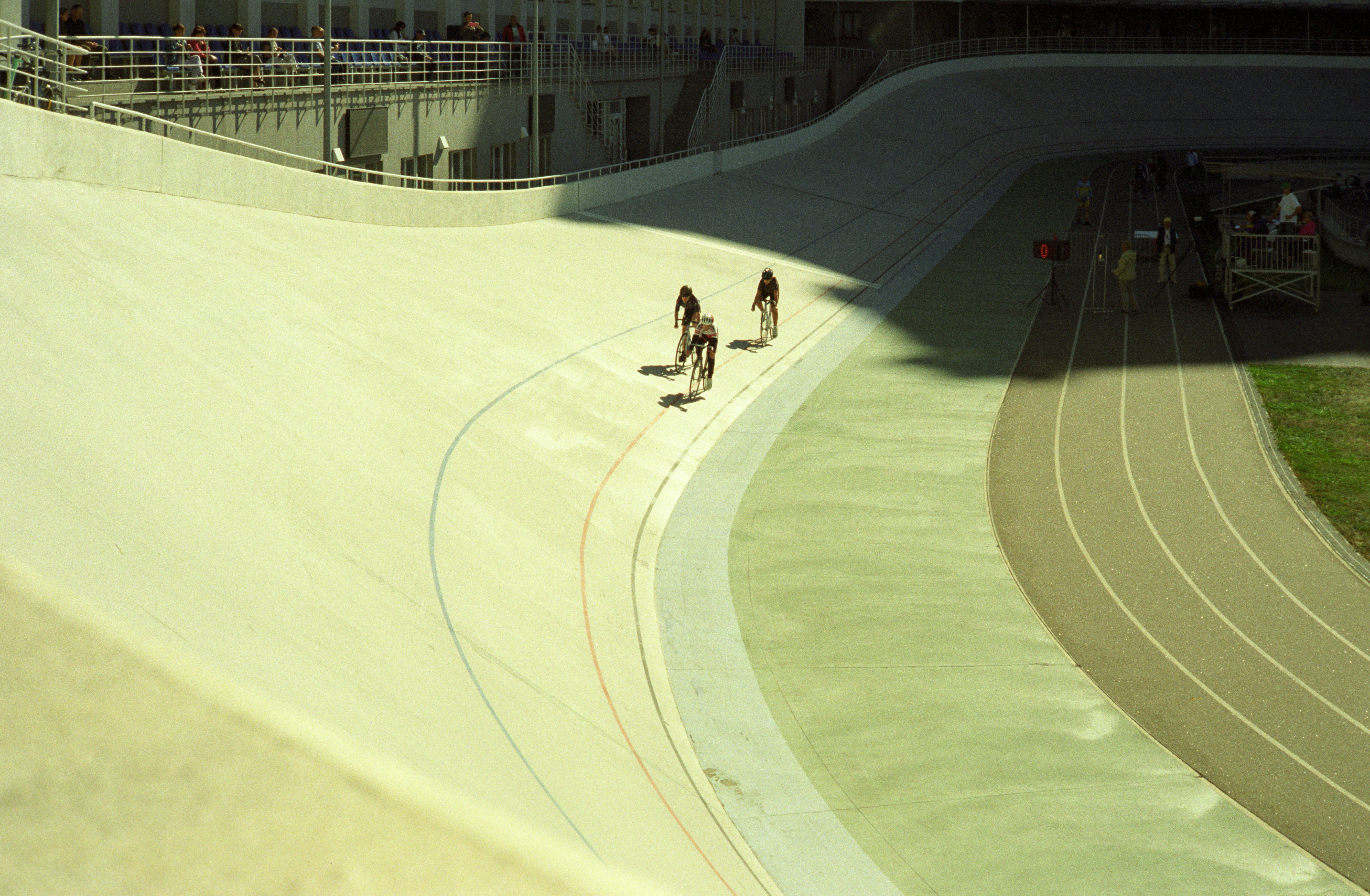 Skaters carve a sunlit bowl under a sweeping concrete arc