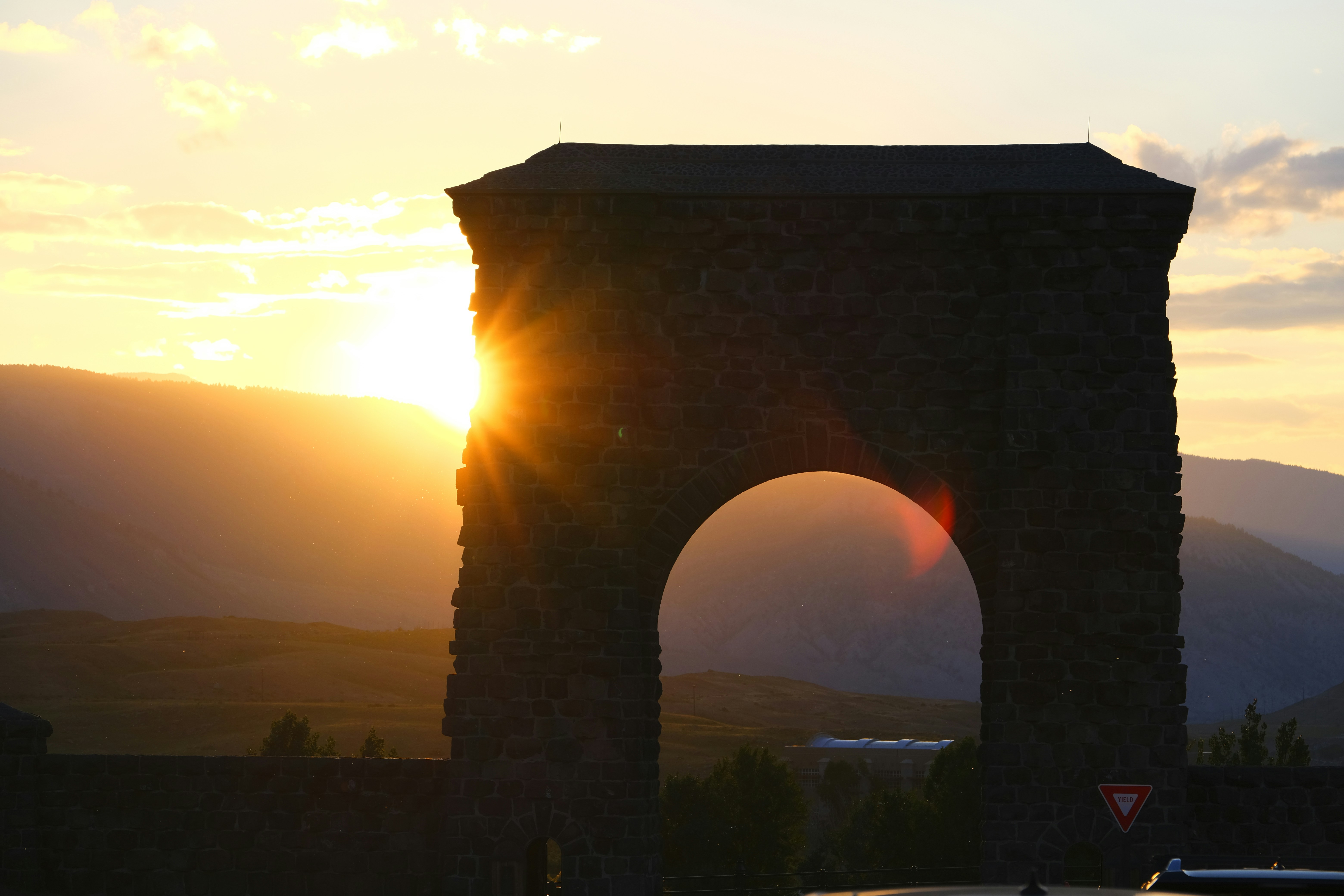 Sun setting behind a large stone arch, casting a warm glow and long shadows across the landscape.