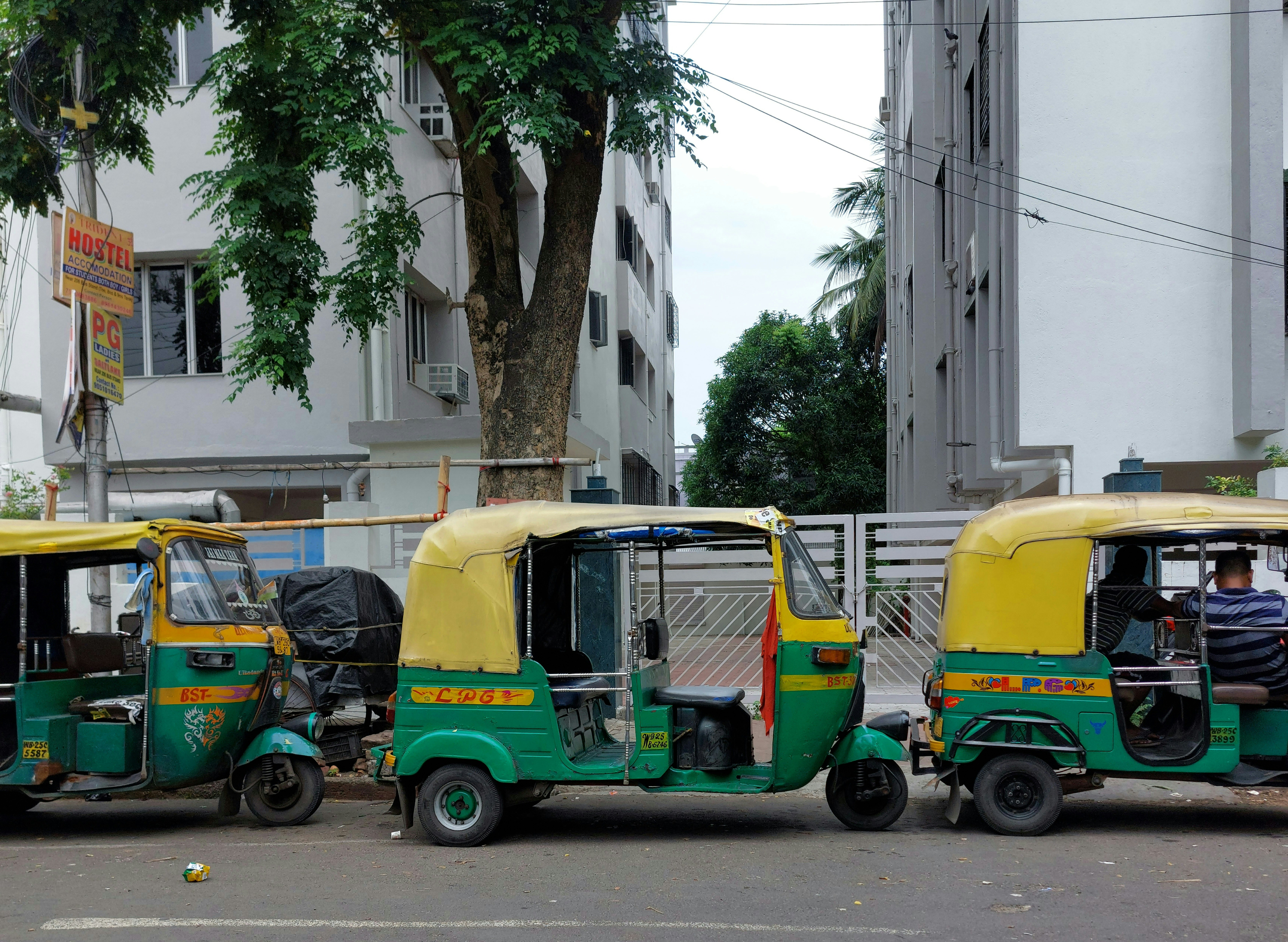 Three green and yellow tuk tuks parked on the side of the road photo ...