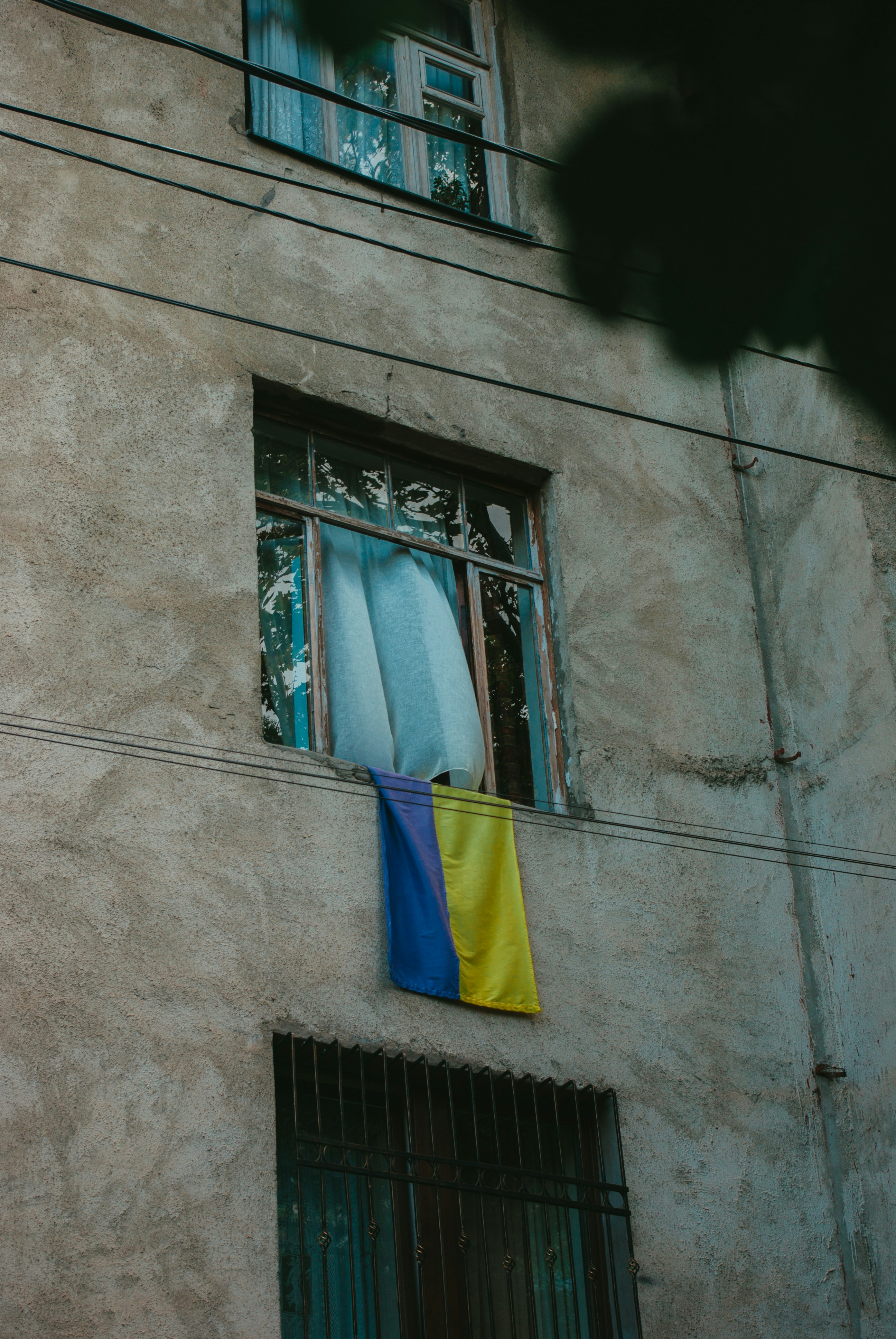 Blue–Yellow Flag Draped from a Weathered Window: A Quiet Urban Moment
