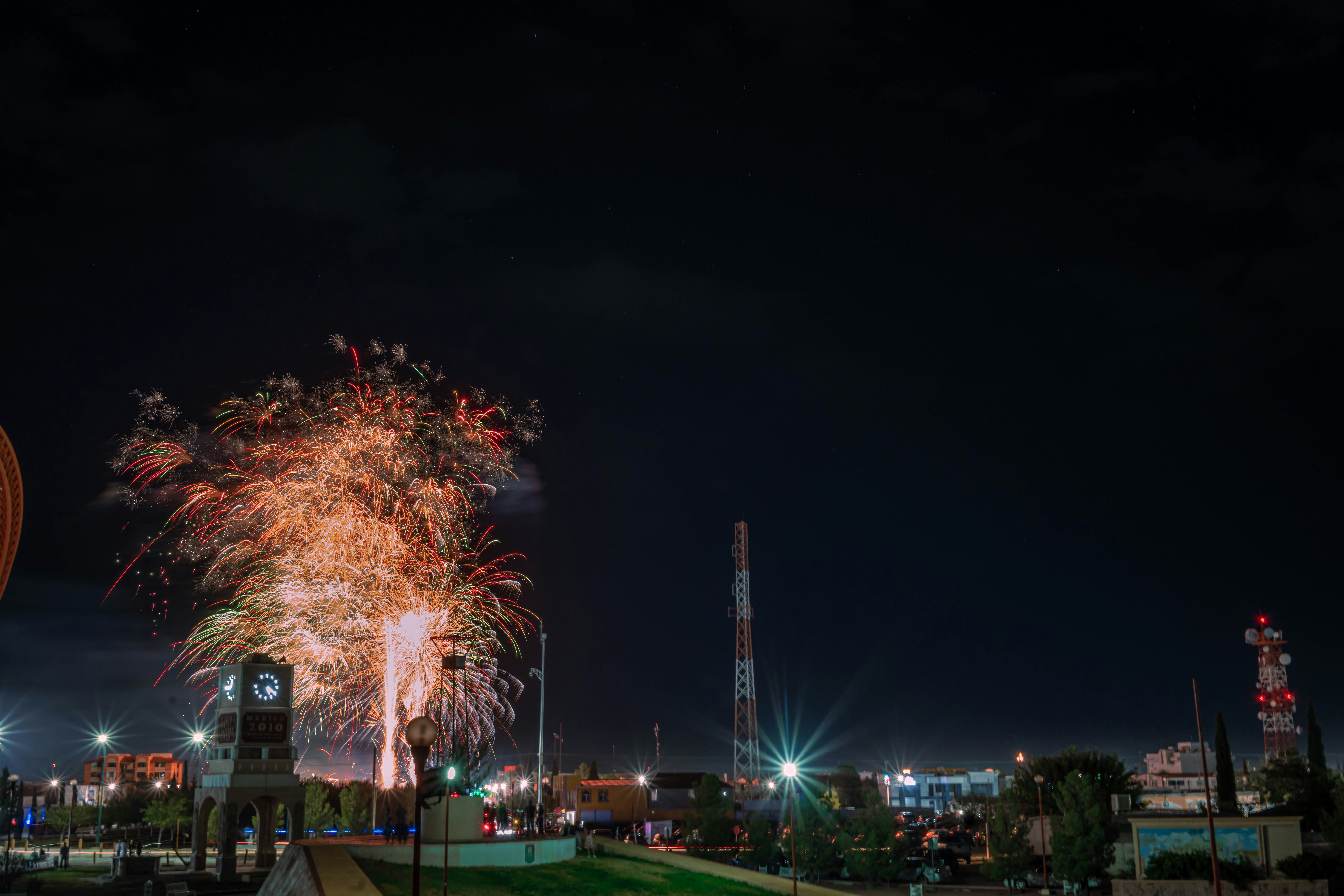 Fireworks burst in vibrant colors over an urban skyline at night.