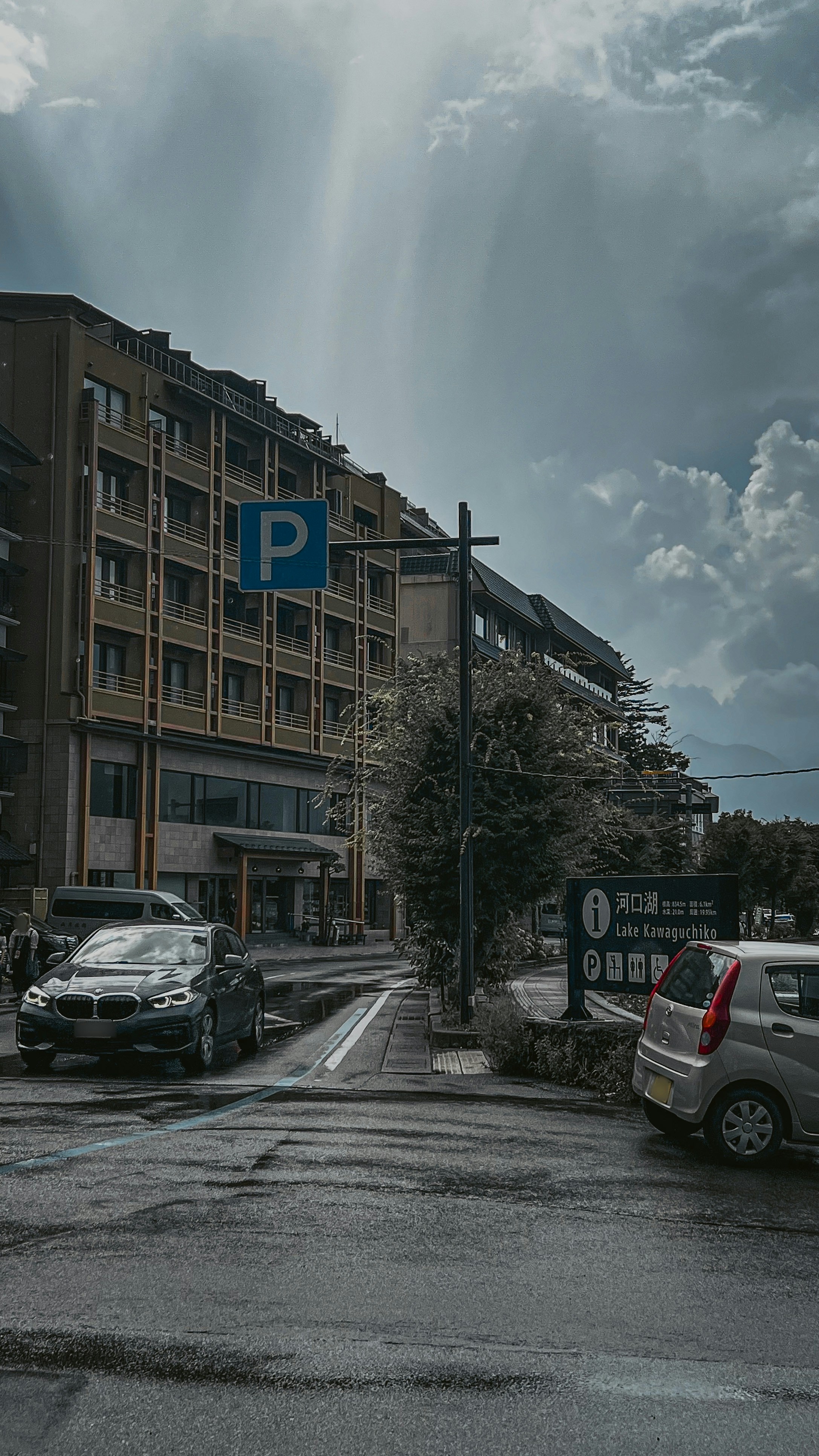A peaceful scene of a quiet city street, captured after a light rain. The wet pavement reflects the soft light, while the surrounding buildings and parked cars create a sense of urban calm. The atmosphere is serene, offering a moment of stillness in the midst of city life.