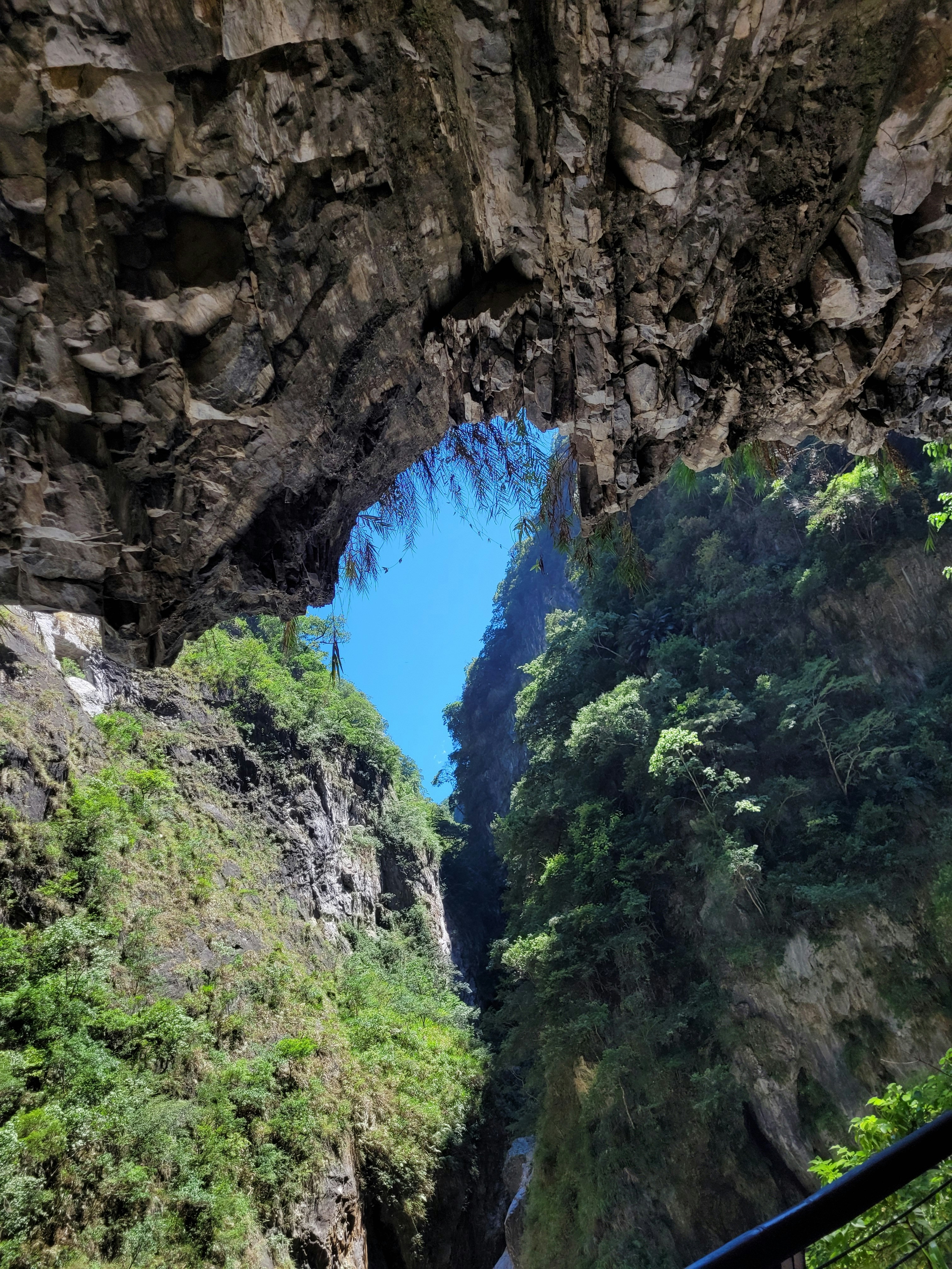A rocky archway frames a lush green valley with cascading water visible below. The vibrant foliage contrasts with the rugged stone, creating a harmonious blend of elements.