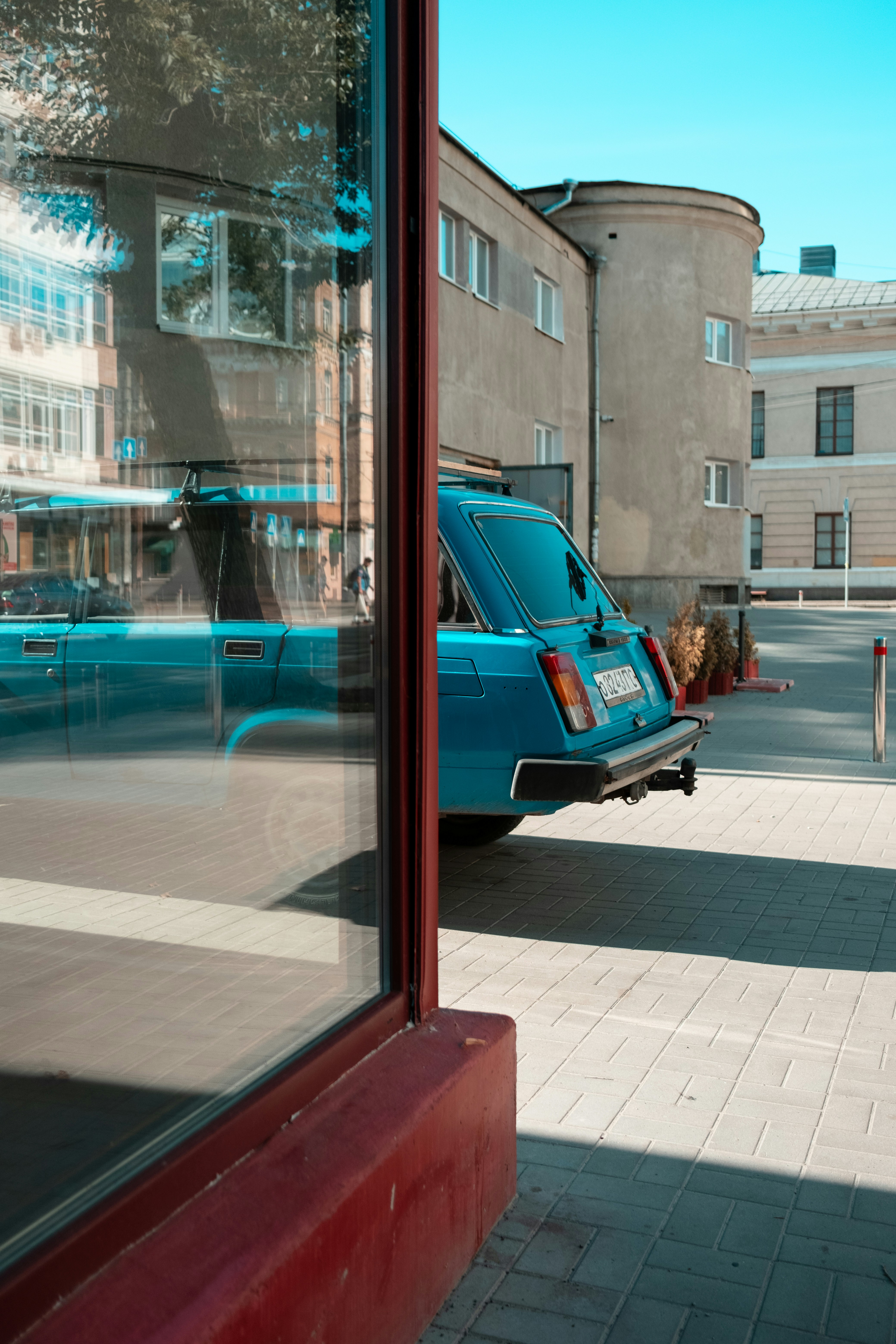 Blue Vintage Sedan Nestled Beside a Glass-Fronted Streetcorner