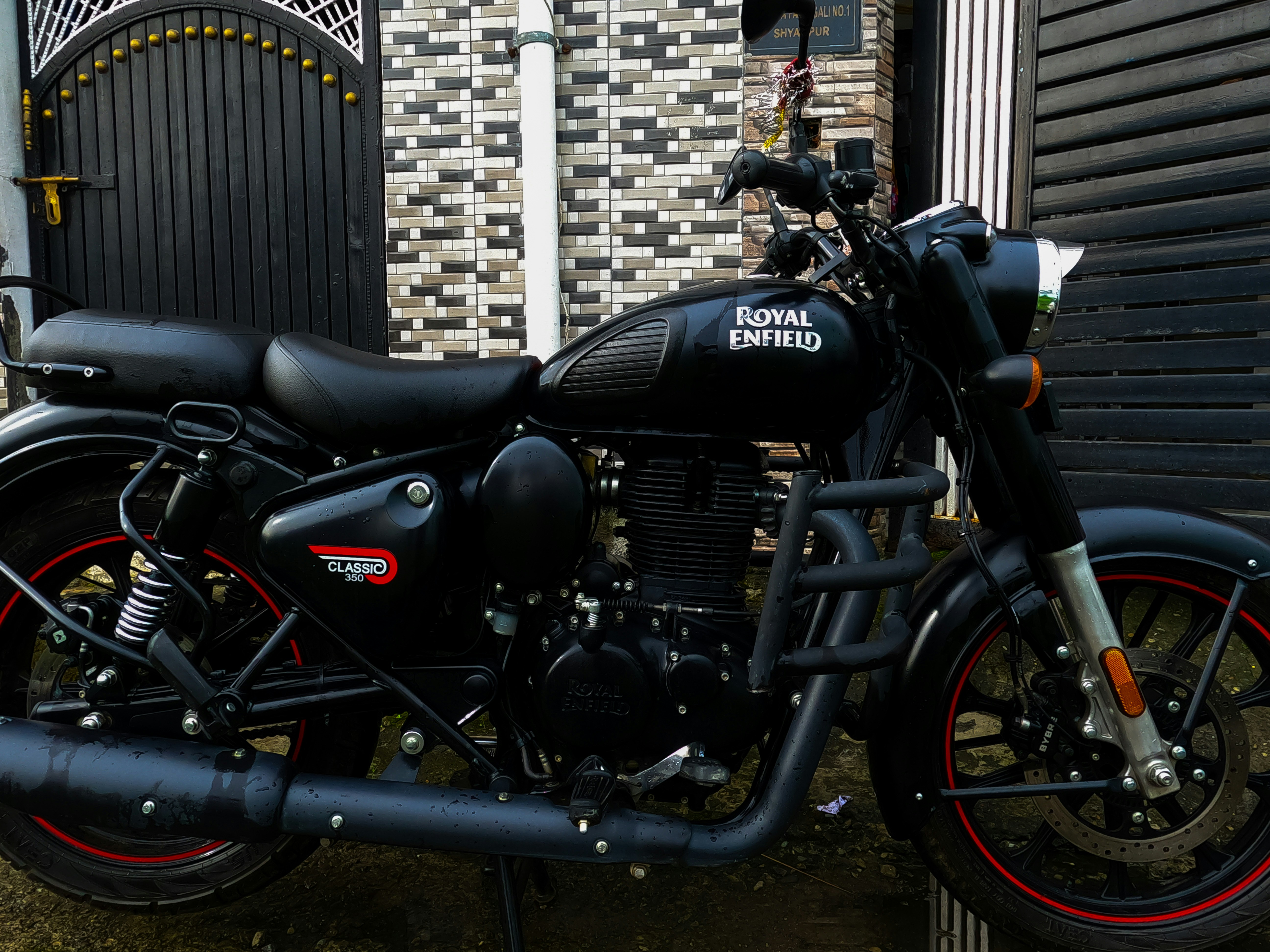 Black Royal Enfield motorcycle parked against a textured wall, showcasing its sleek design and classic features.