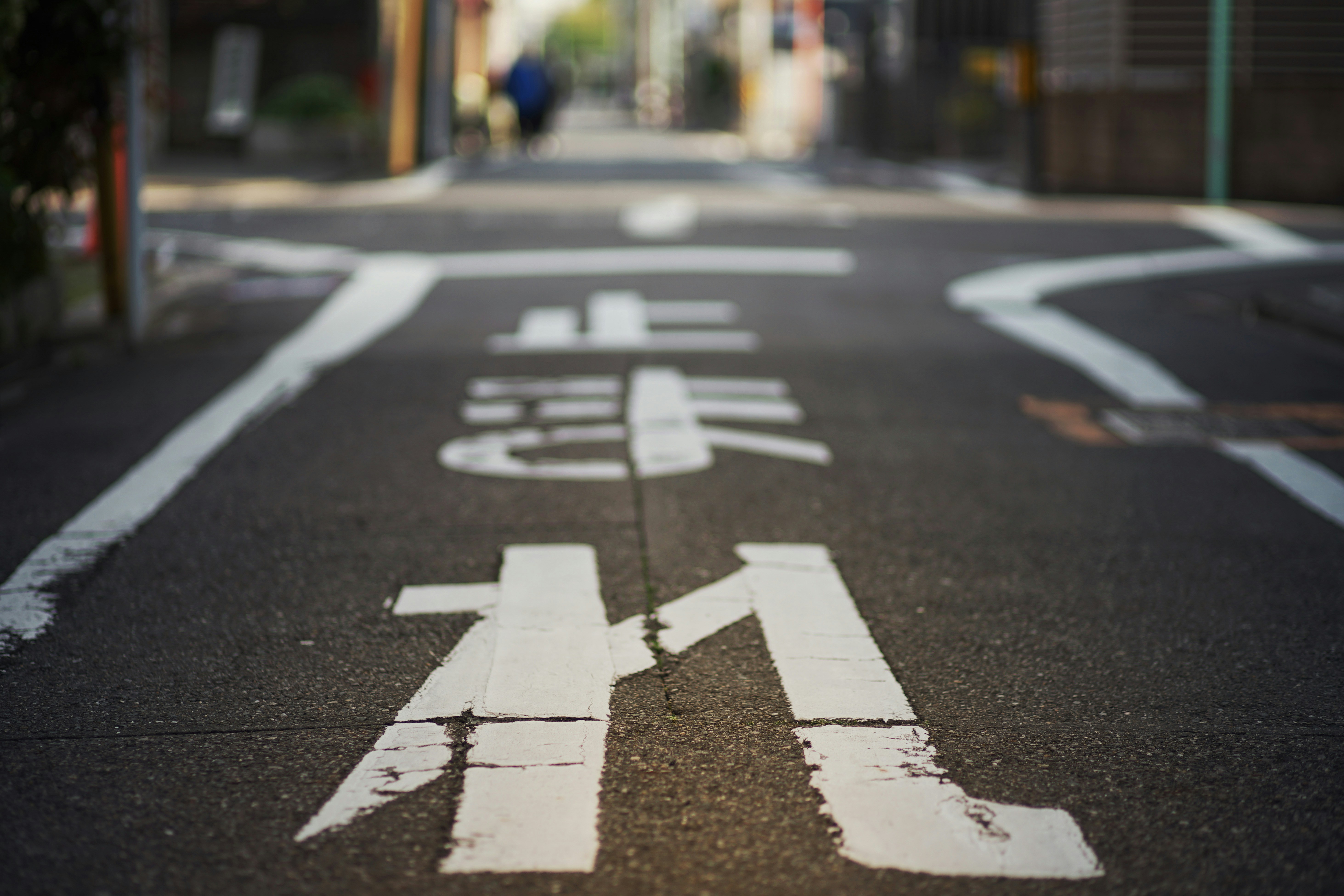 Blurred city street view with Japanese road markings and distant figure.