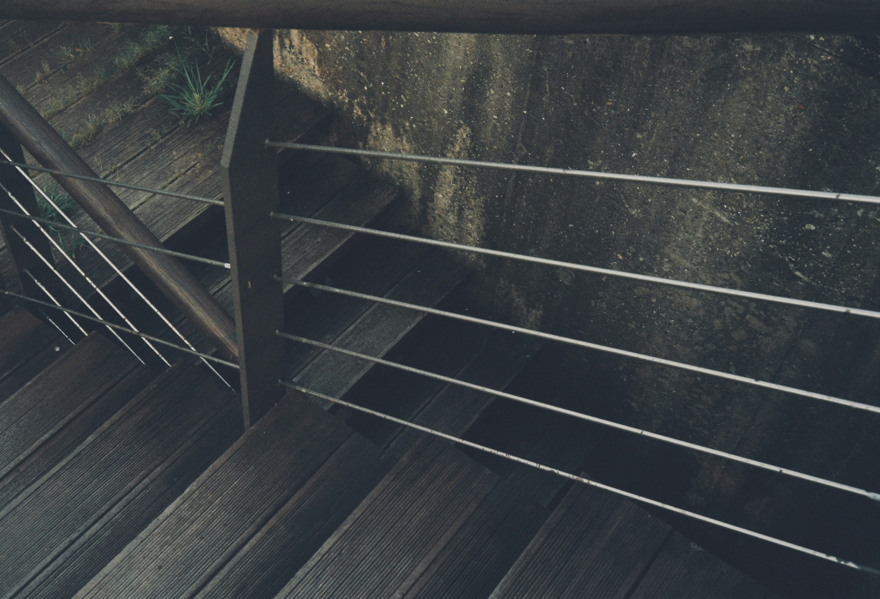 Wooden staircase with sleek metal railings leading downward, illuminated by soft ambient light. Textured wall in the background adds depth.