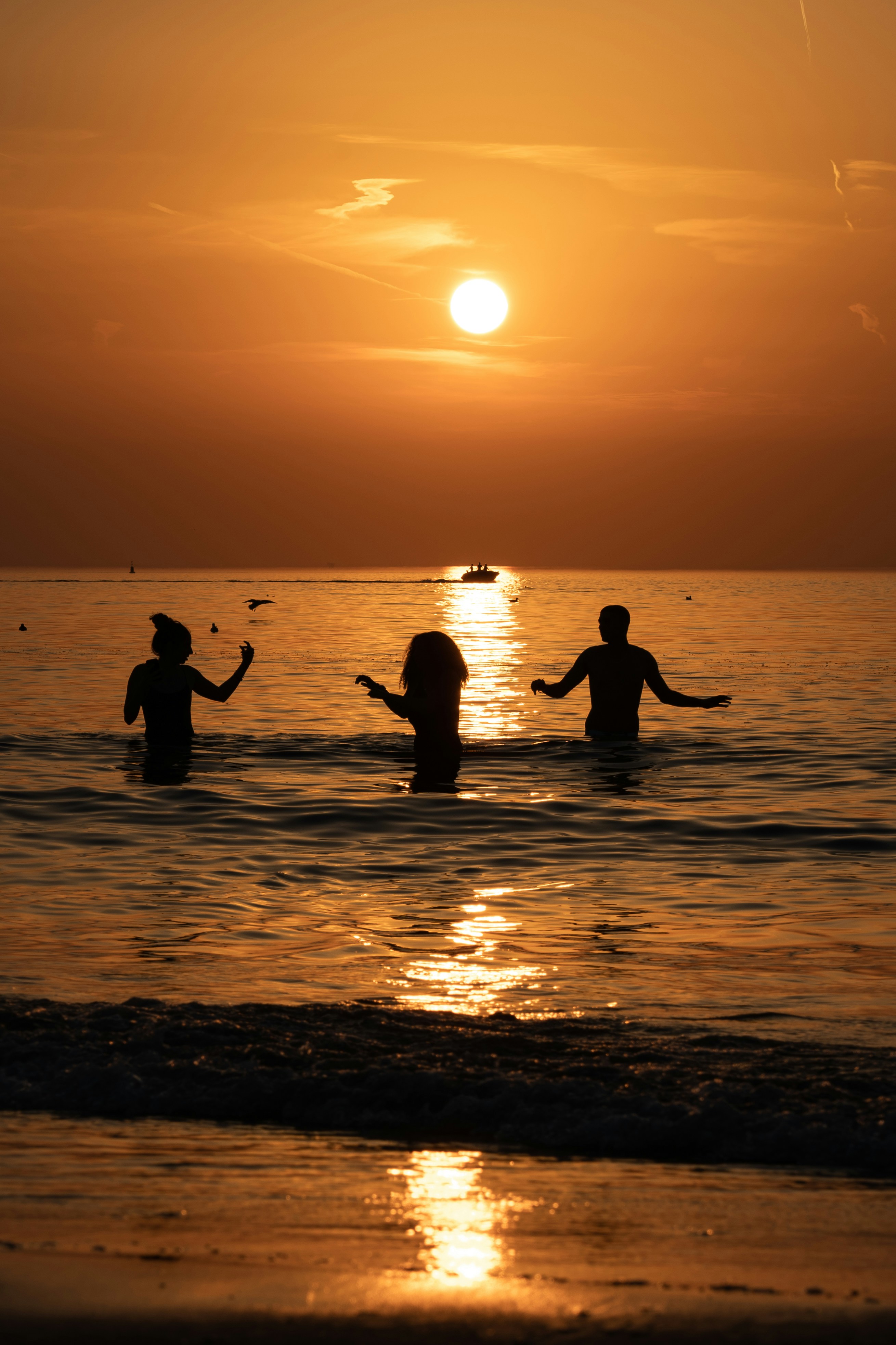 A group of people wading in the ocean at sunset photo – Free ...
