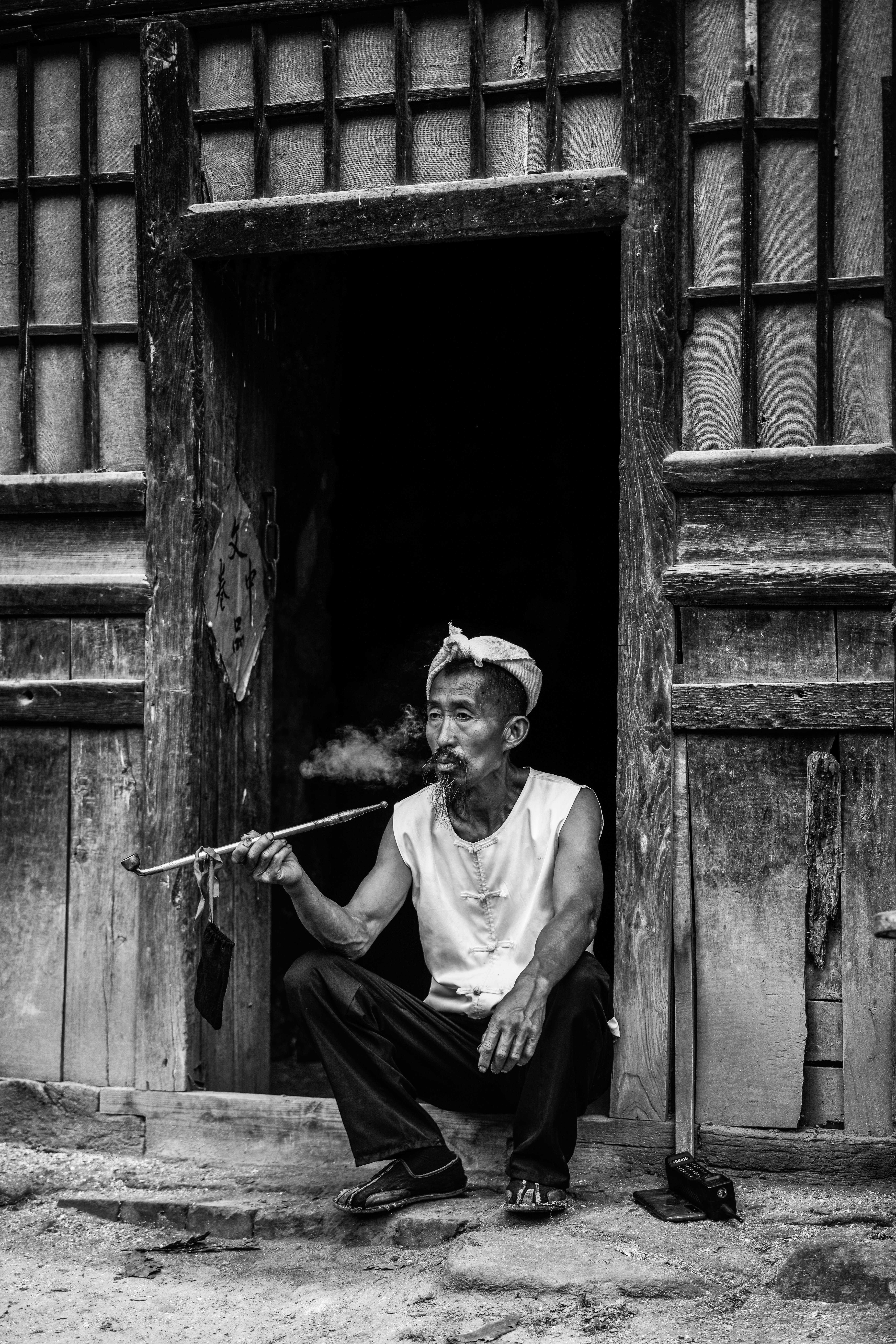 A man sitting in a doorway smoking a pipe photo – Free China Image on ...