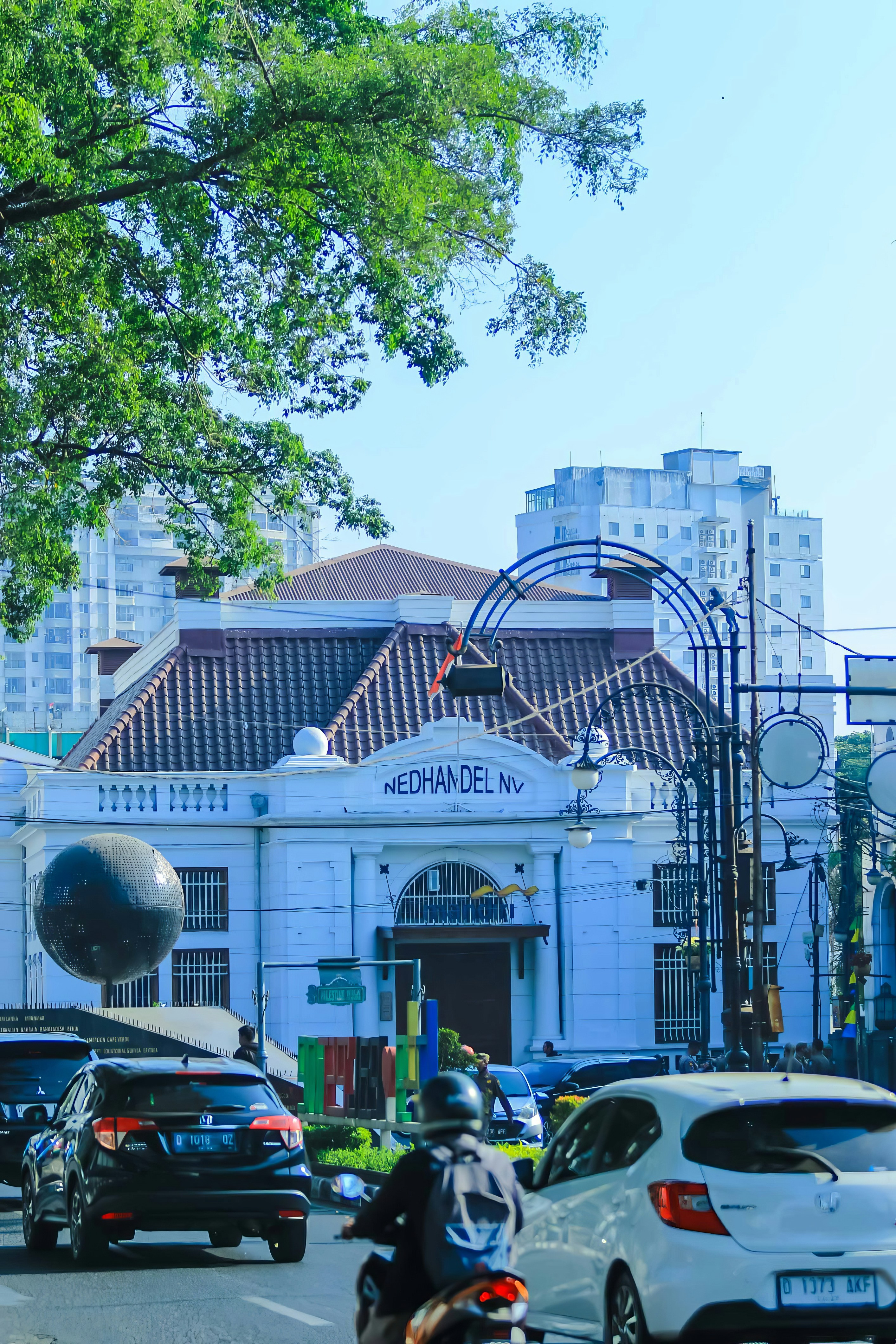 Neoclassical facade at a busy urban crossroads under a canopy of green