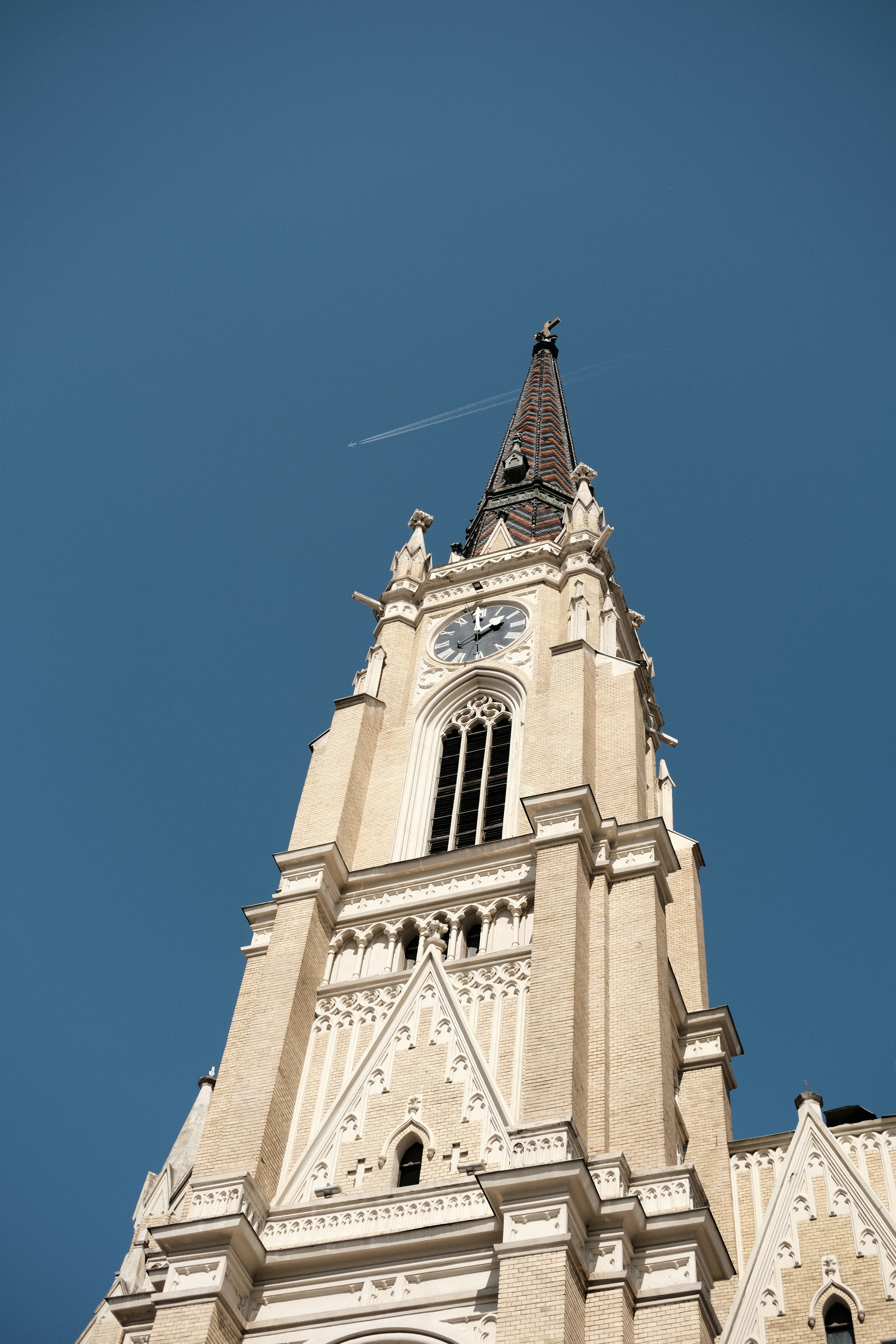 Historic church tower reaching skyward against a clear blue backdrop, showcasing intricate architectural details and a clock face.