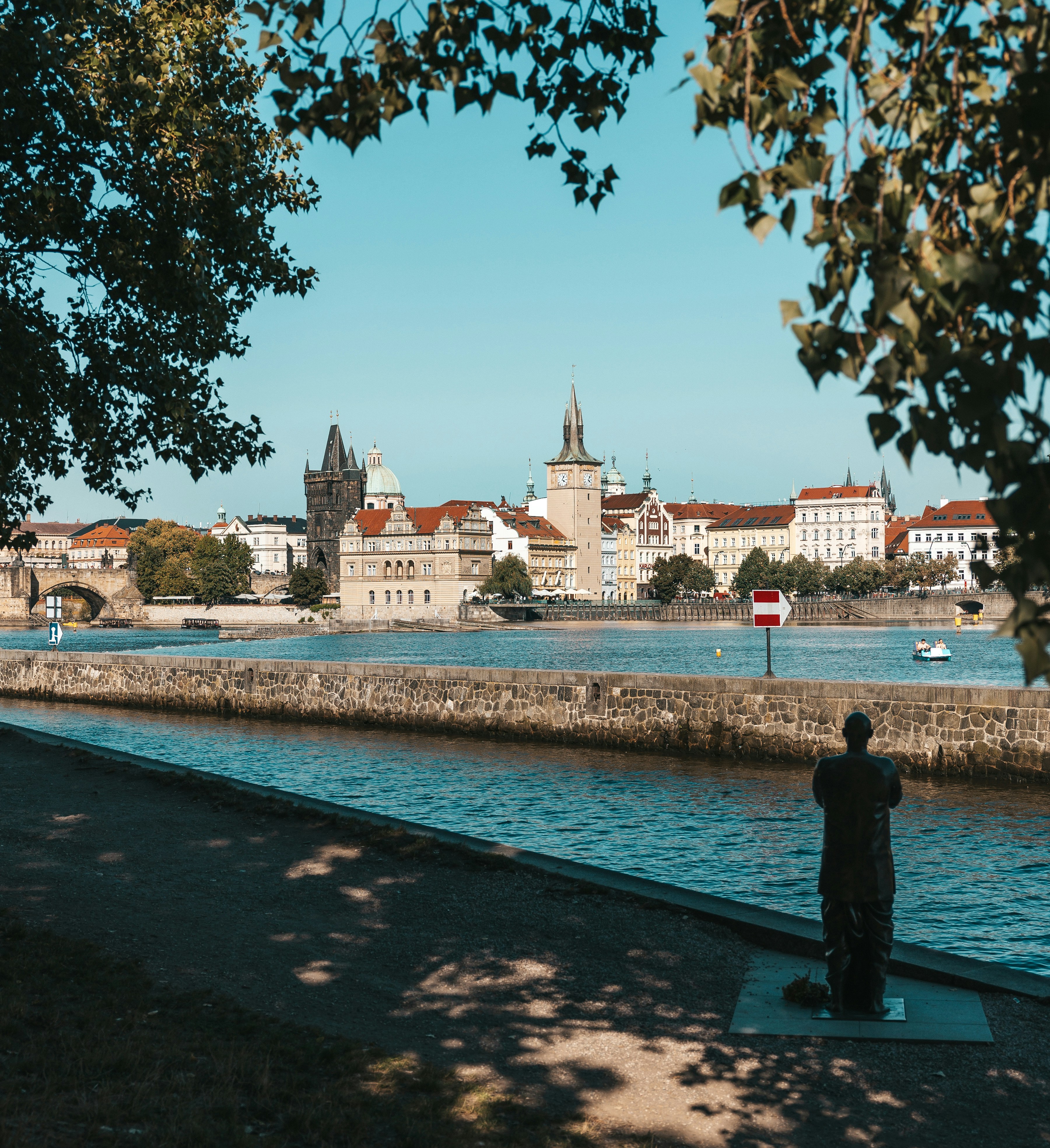 Riverside Sentinel: Bronze Statue Framing a Sunlit Historic City Across the Water
