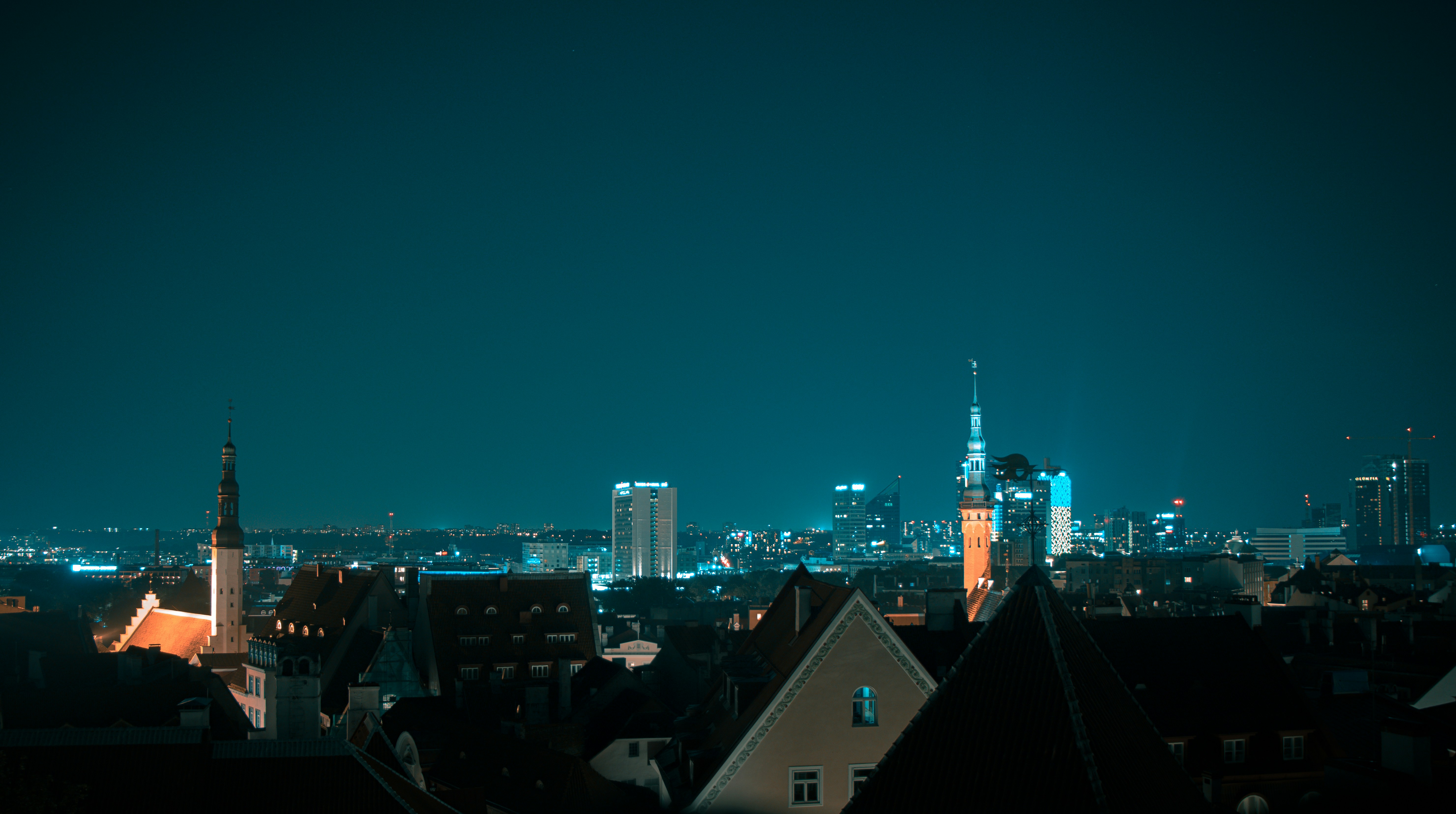 City skyline at night with illuminated buildings and church spires under a deep blue sky.