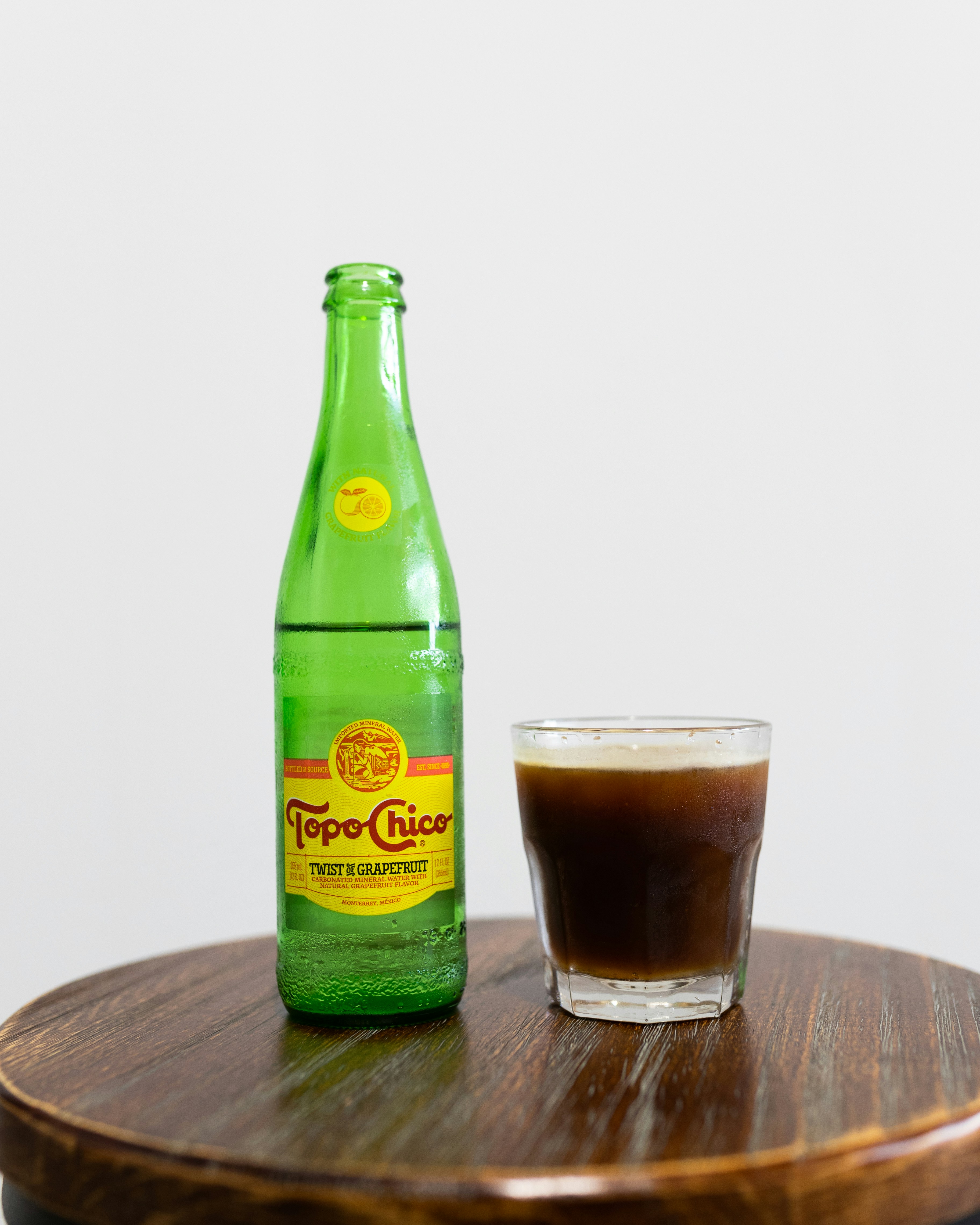 Emerald Topo Chico and a Glass of Cola on a Round Wooden Table