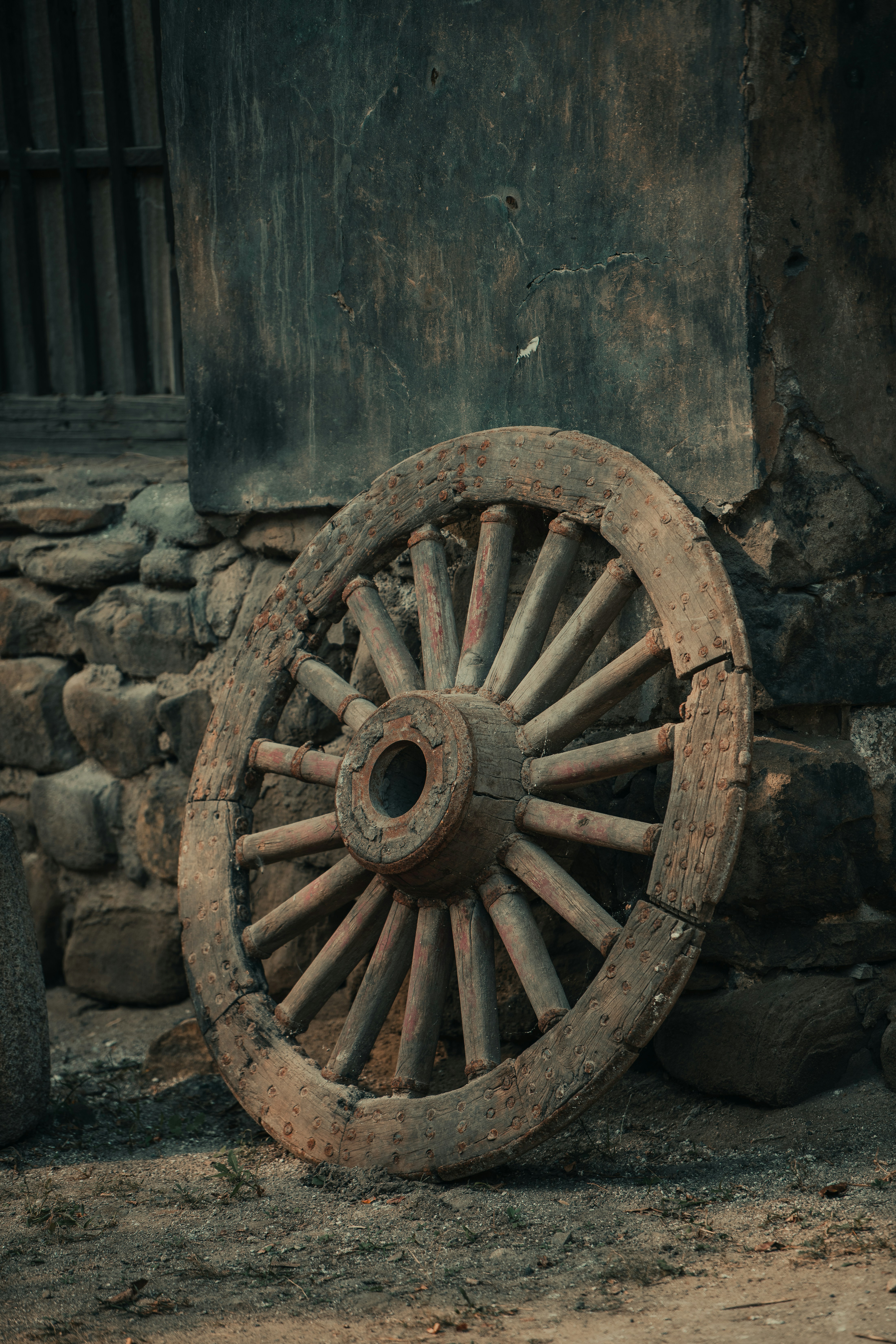 Rust and Stone: An Old Wagon Wheel Resting by a Weathered Wall
