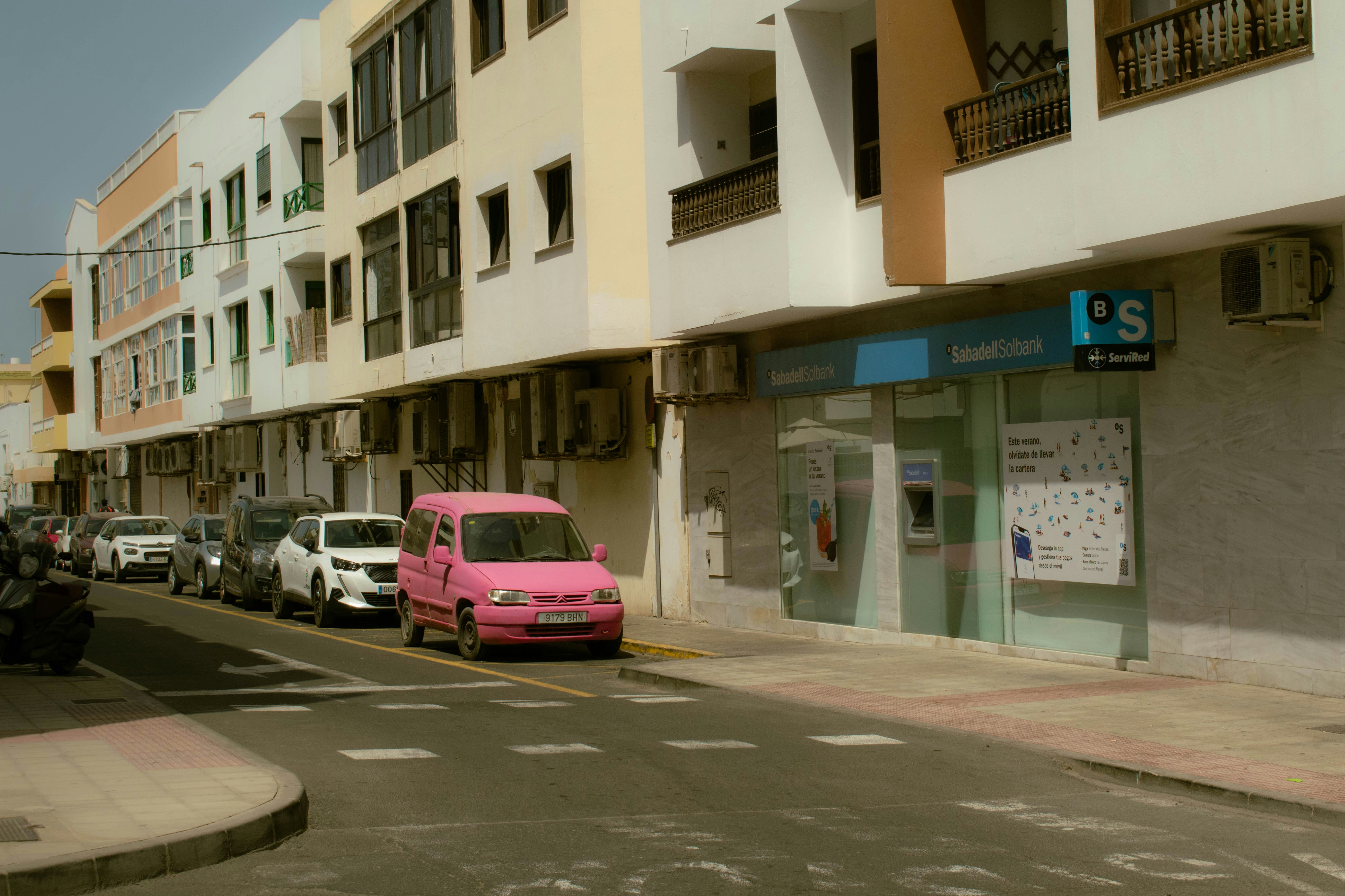 Pink van parked along a quiet street beside a bank in Fuerteventura, Spain.