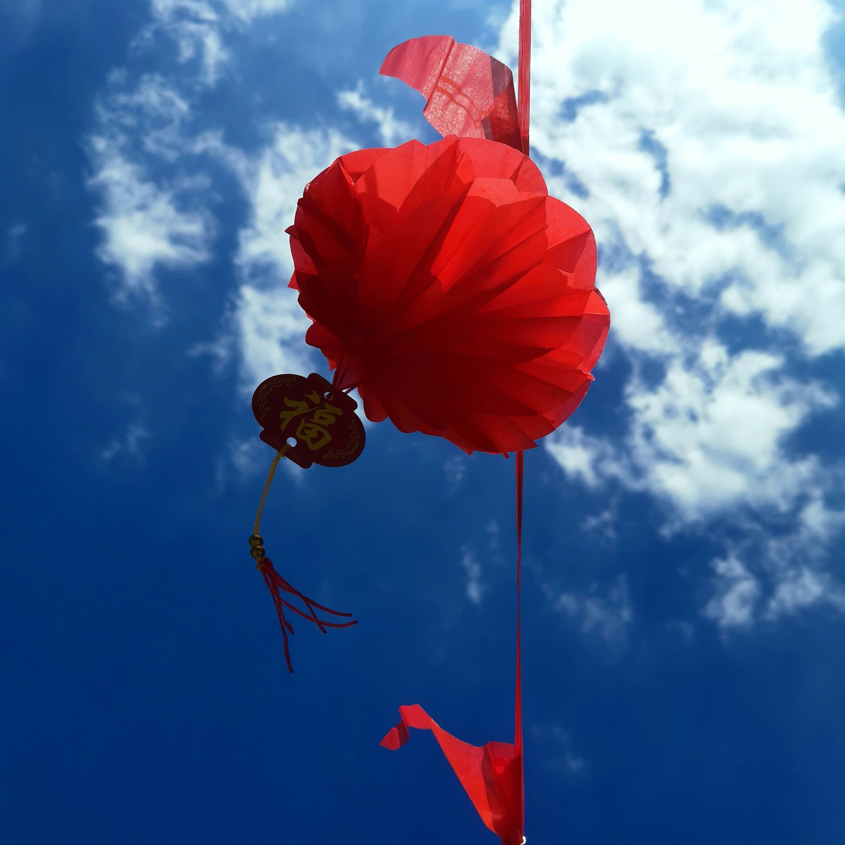 A vibrant red lantern sways gently against a backdrop of fluffy clouds, embodying the spirit of celebration. The intricate details of the lantern add a cultural touch to the scene.