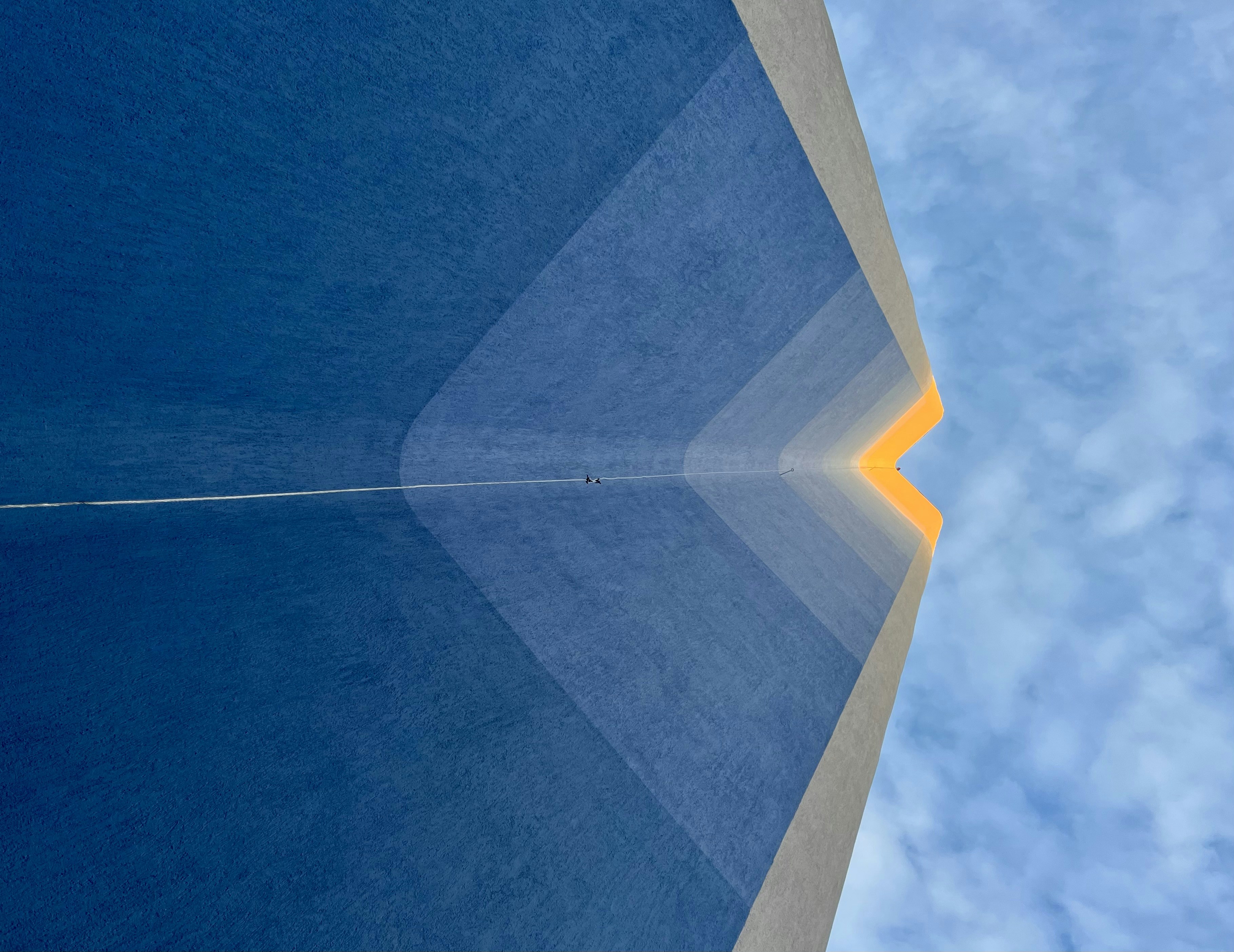 Blue geometric facade converges toward a glowing orange notch against a bright blue sky.