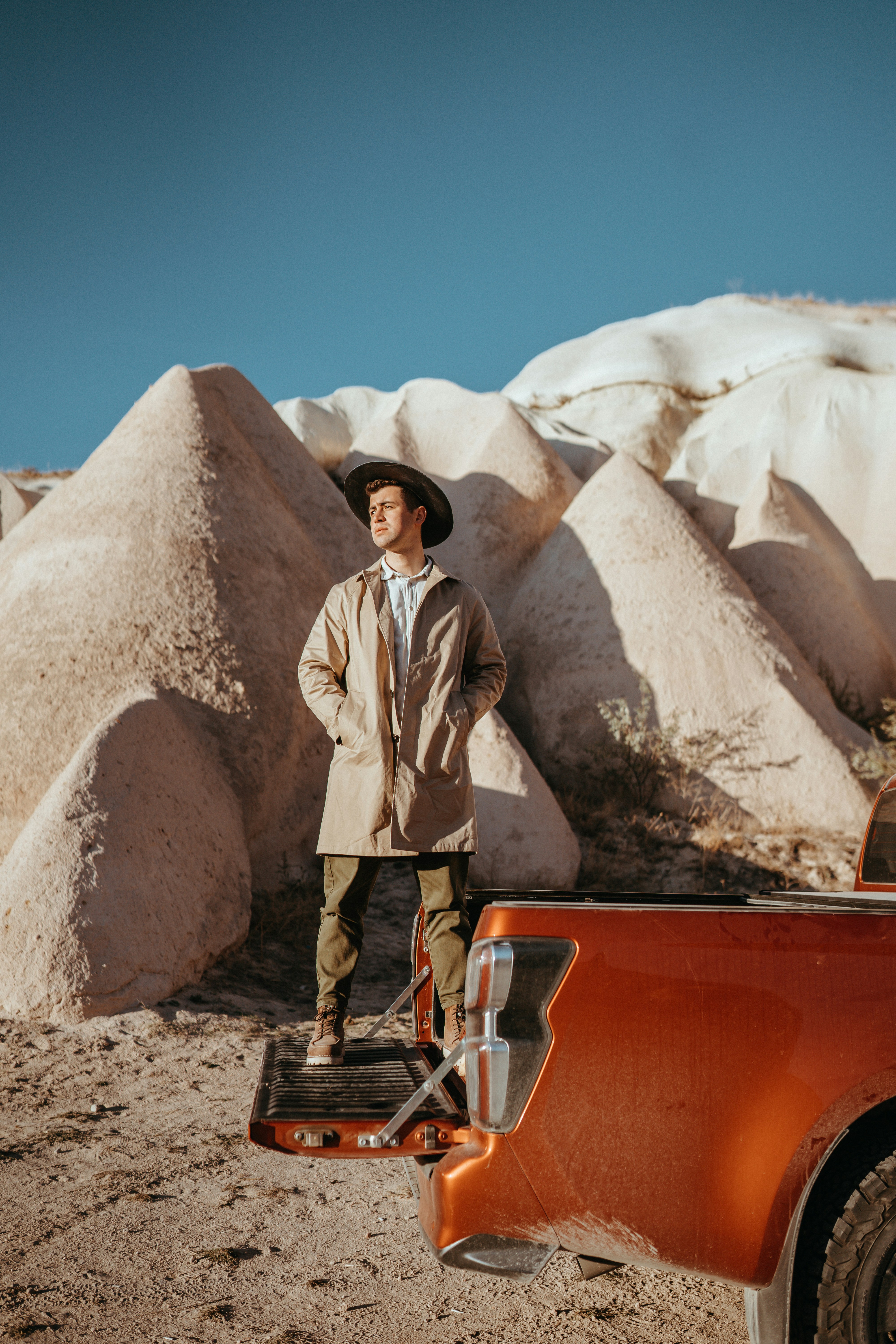 Dusty Horizons: A Man in Beige Standing by a Bright Orange Truck