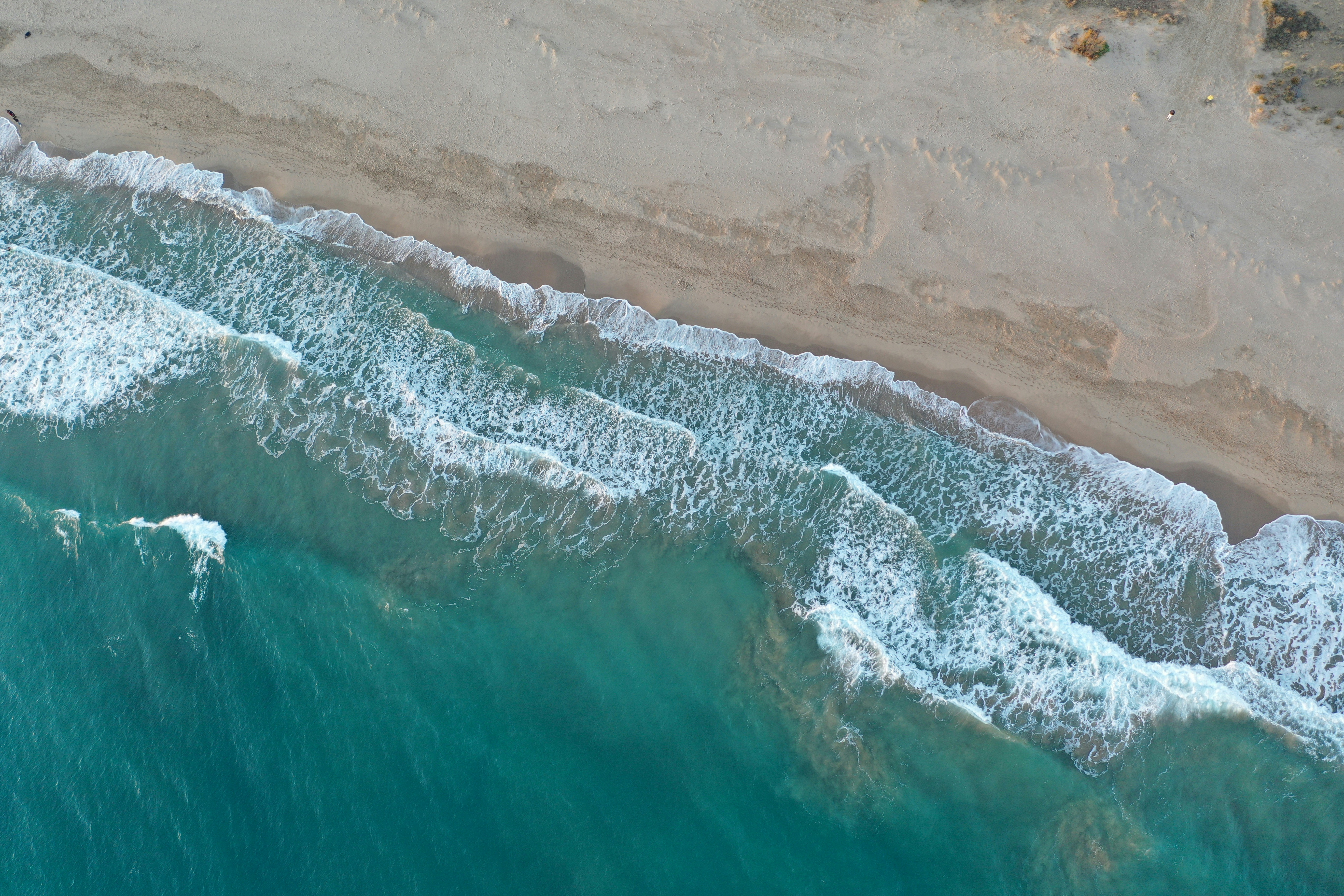 Aerial view of turquoise waves gently crashing onto a sandy beach.