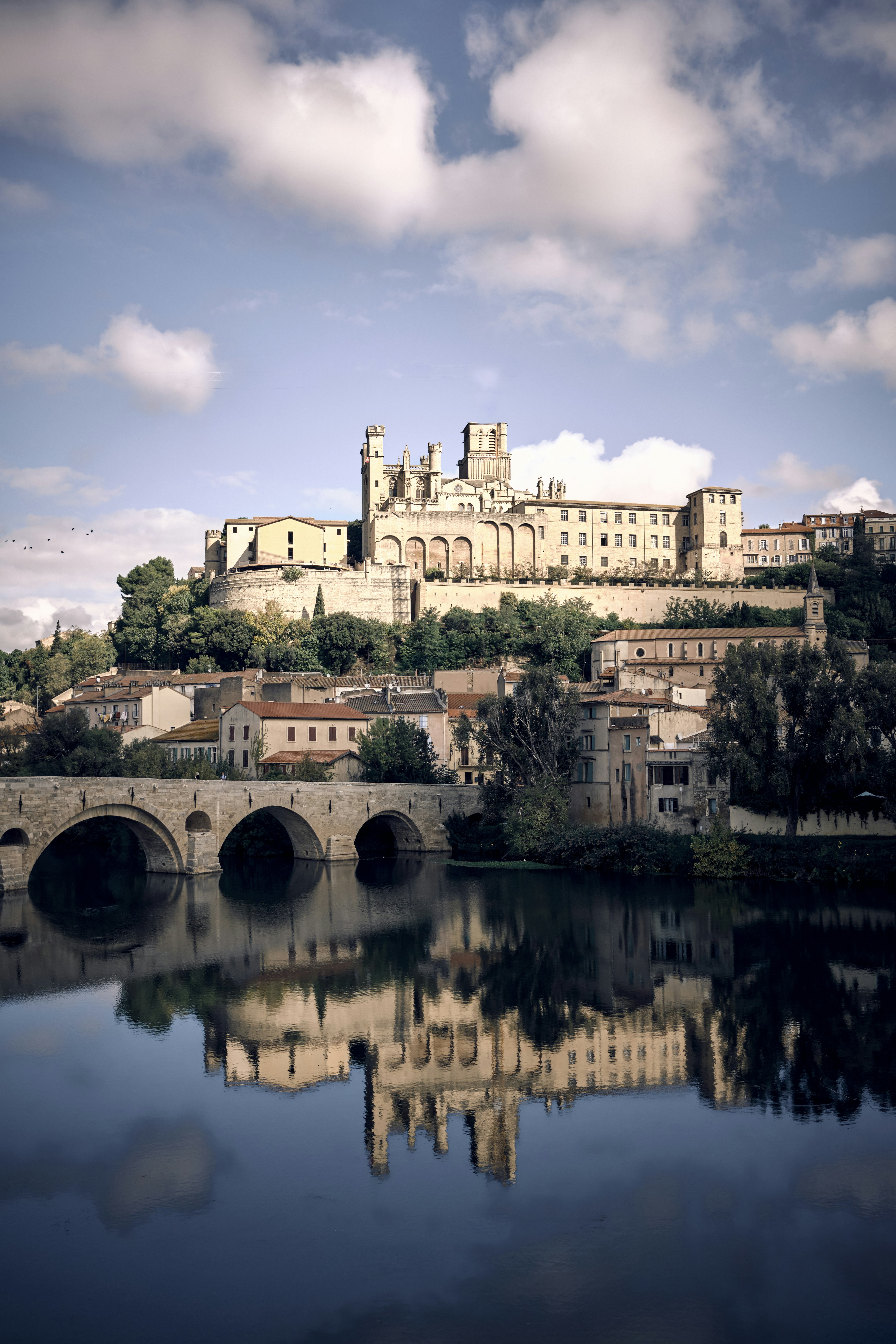 Captivating bridge connecting cityscape, with stunning sunset, reflecting in serene river. Historic architecture reflects on river in scenic city of Béziers.